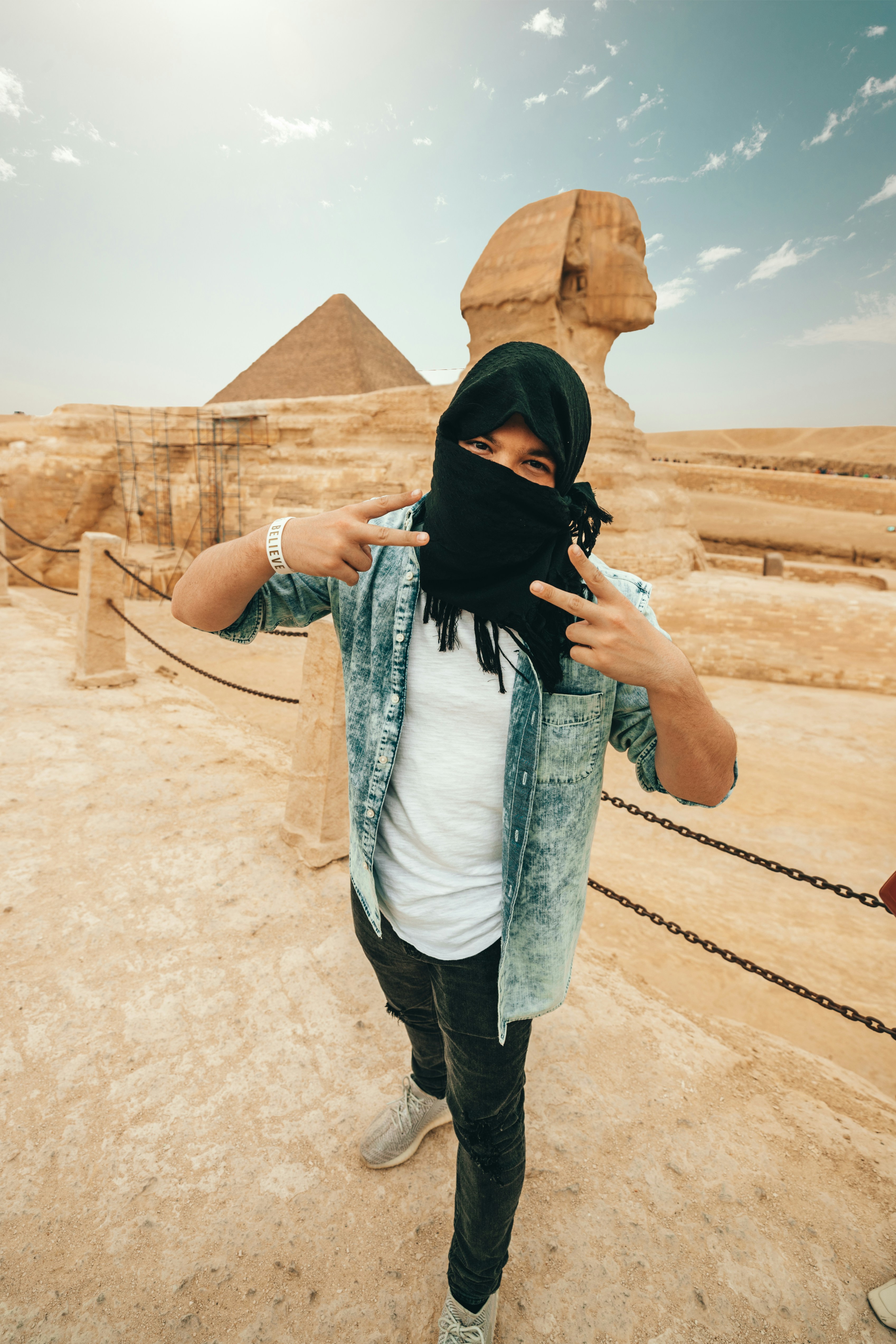Individual posing playfully in front of the Sphinx and pyramids, showcasing a blend of ancient history and contemporary style.