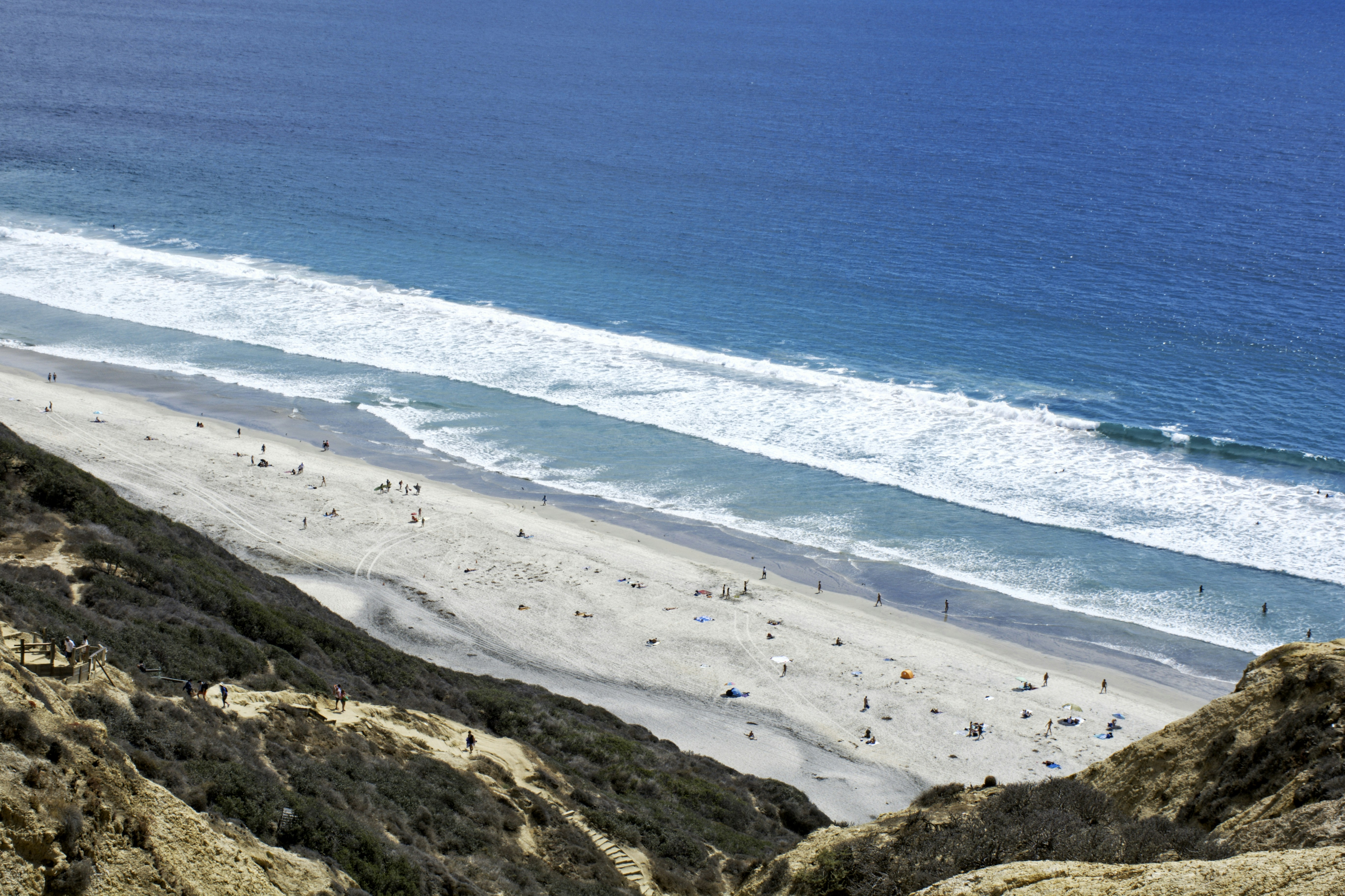 Aerial view of people scattered along a sandy beach with waves lapping the shore.