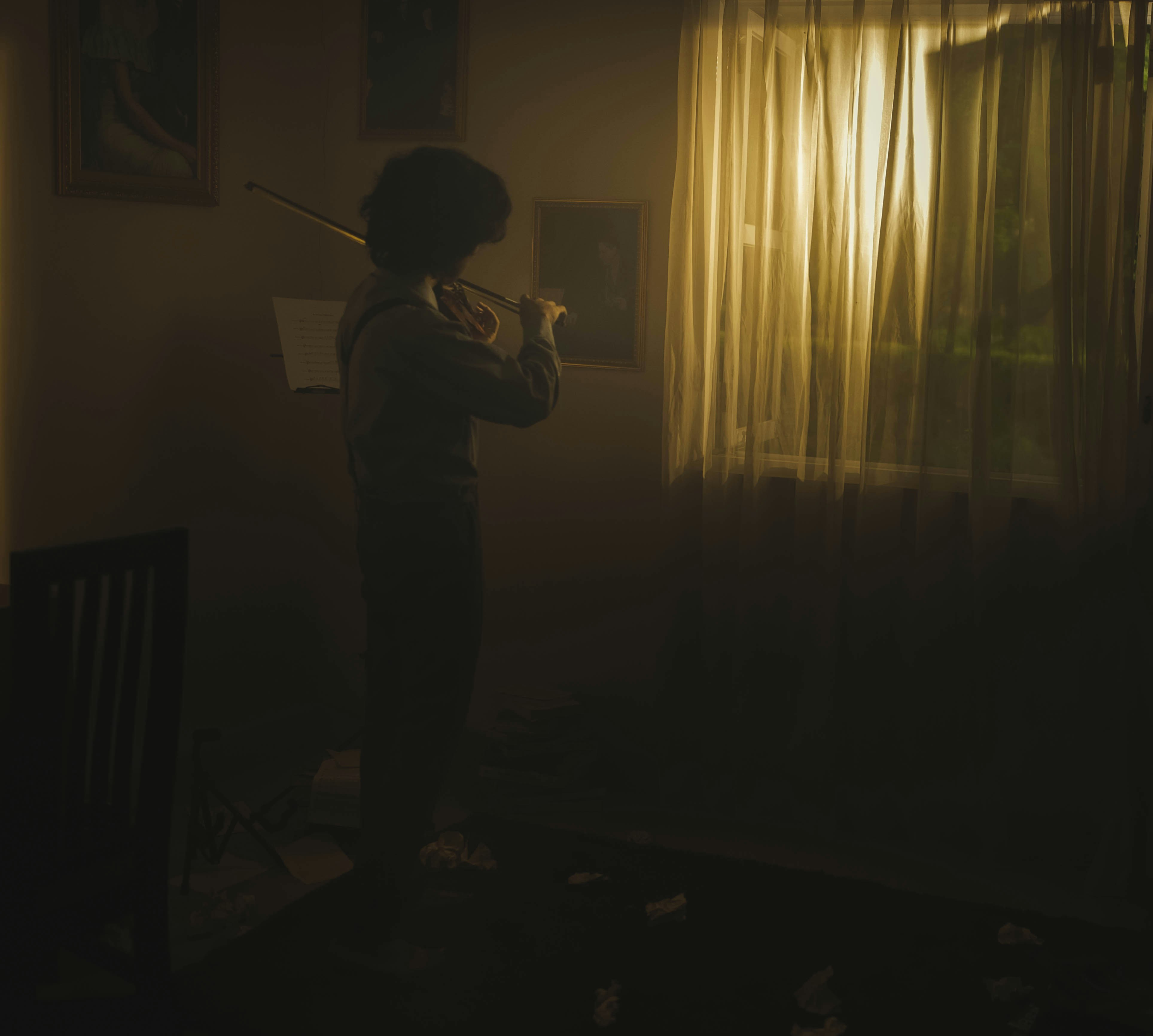 A young musician playing the flute in a dimly lit room, with soft sunlight filtering through sheer curtains, creating a warm atmosphere.