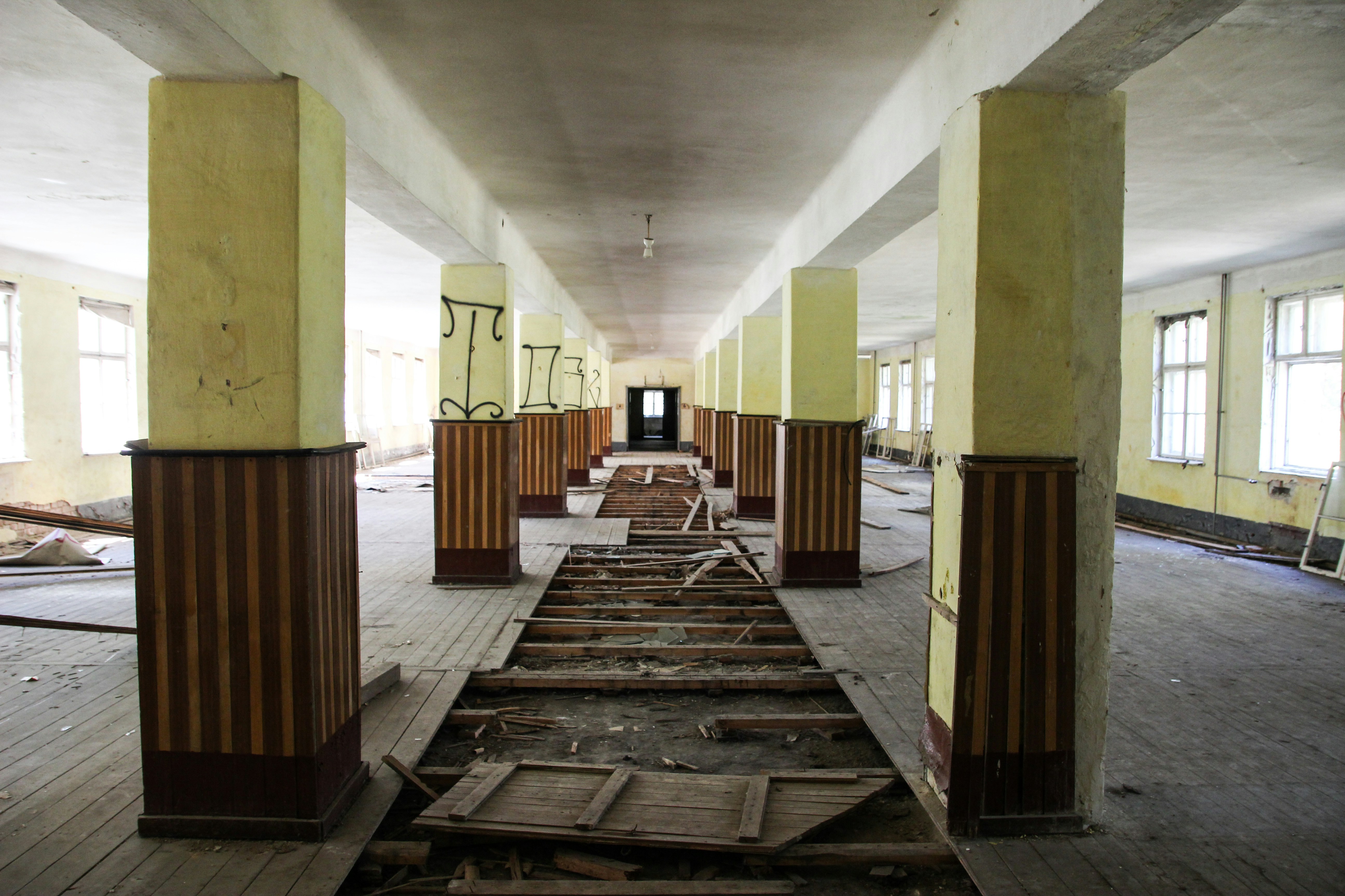 Desolate interior of an abandoned building featuring exposed wooden floorboards and faded yellow walls.