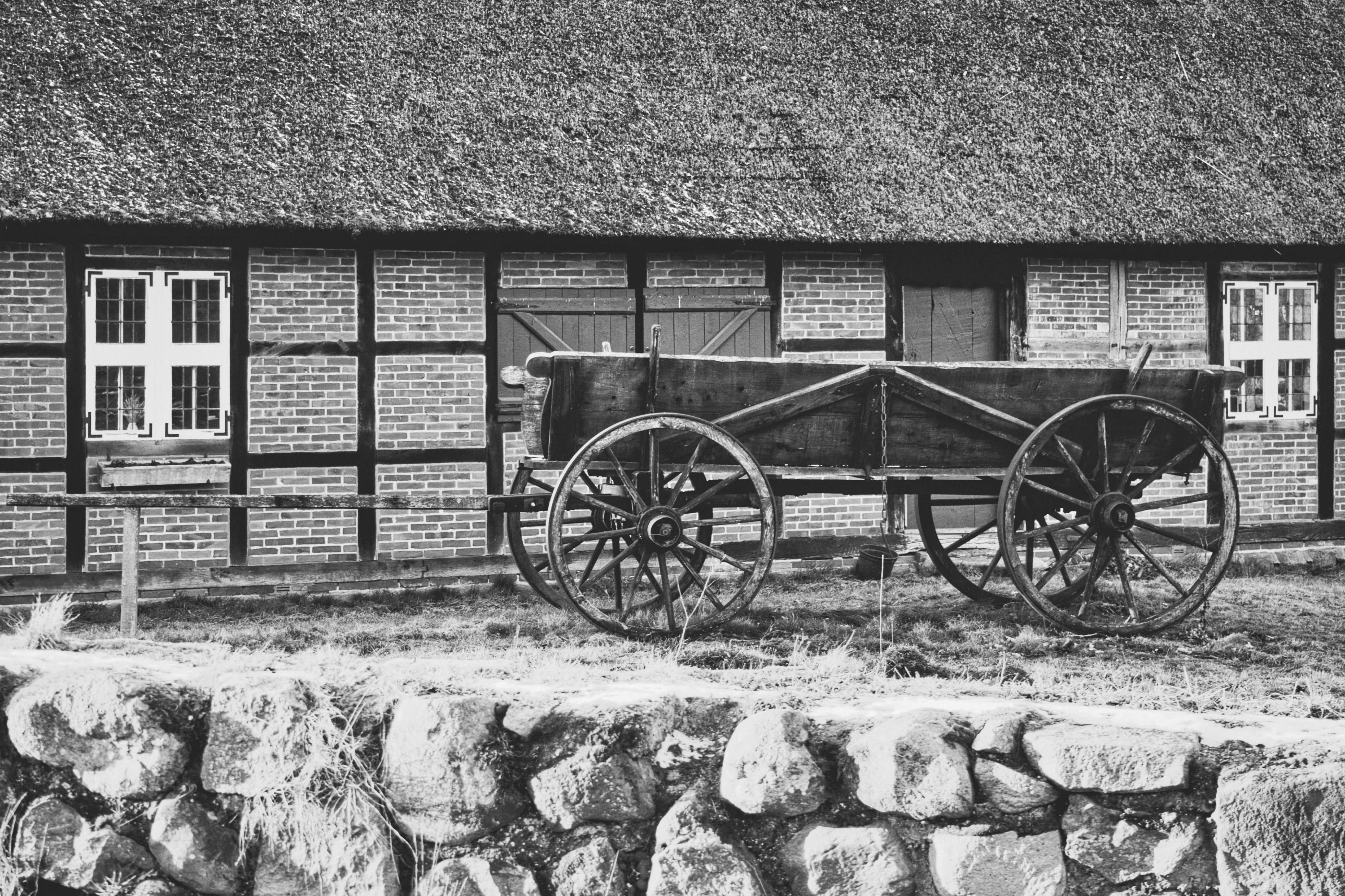 Weathered wooden cart resting beside a traditional thatched-roof building, showcasing historical craftsmanship and rural charm.