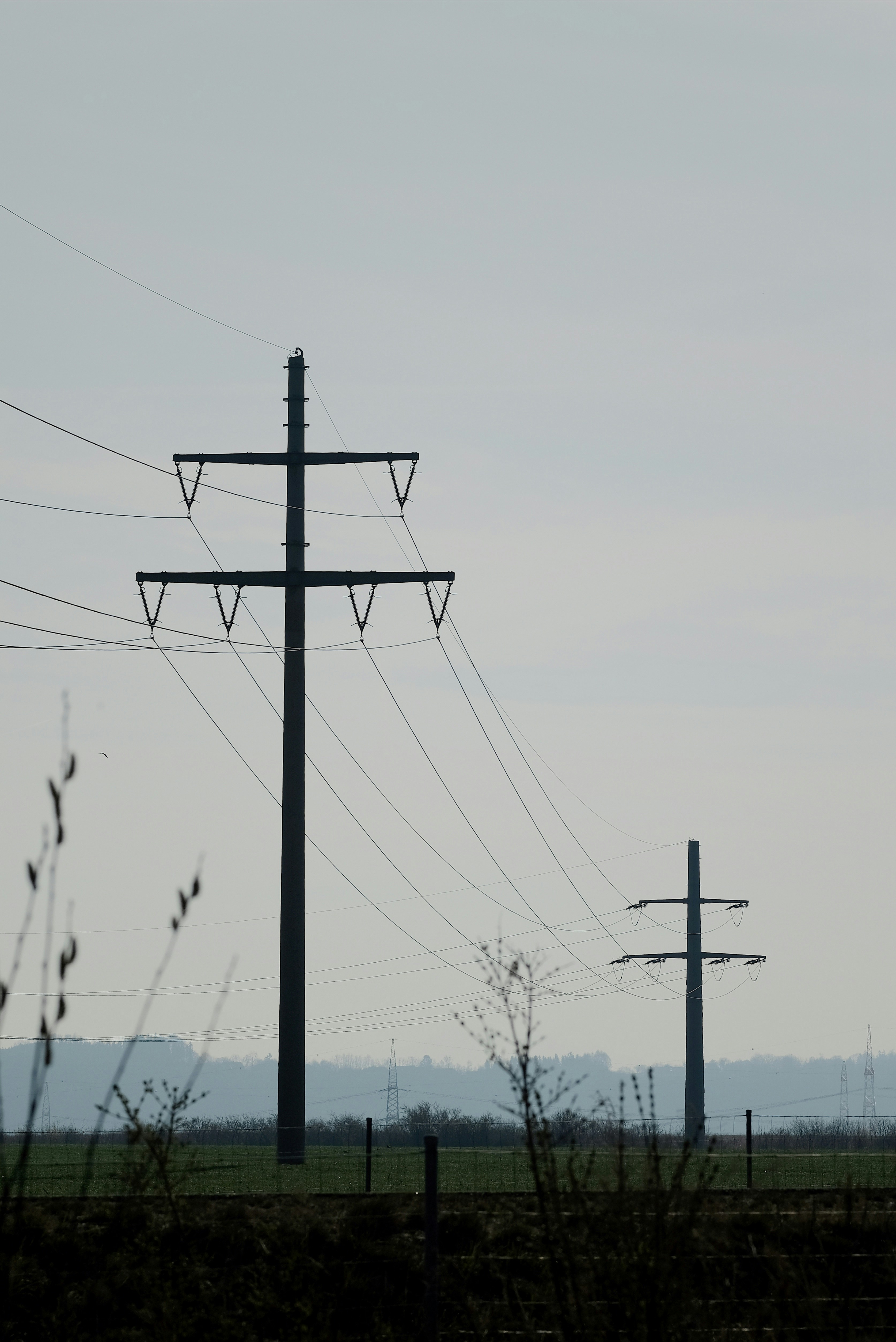 Silhouetted power poles stand against a muted sky, their lines stretching across the landscape. The scene captures the essence of rural infrastructure.