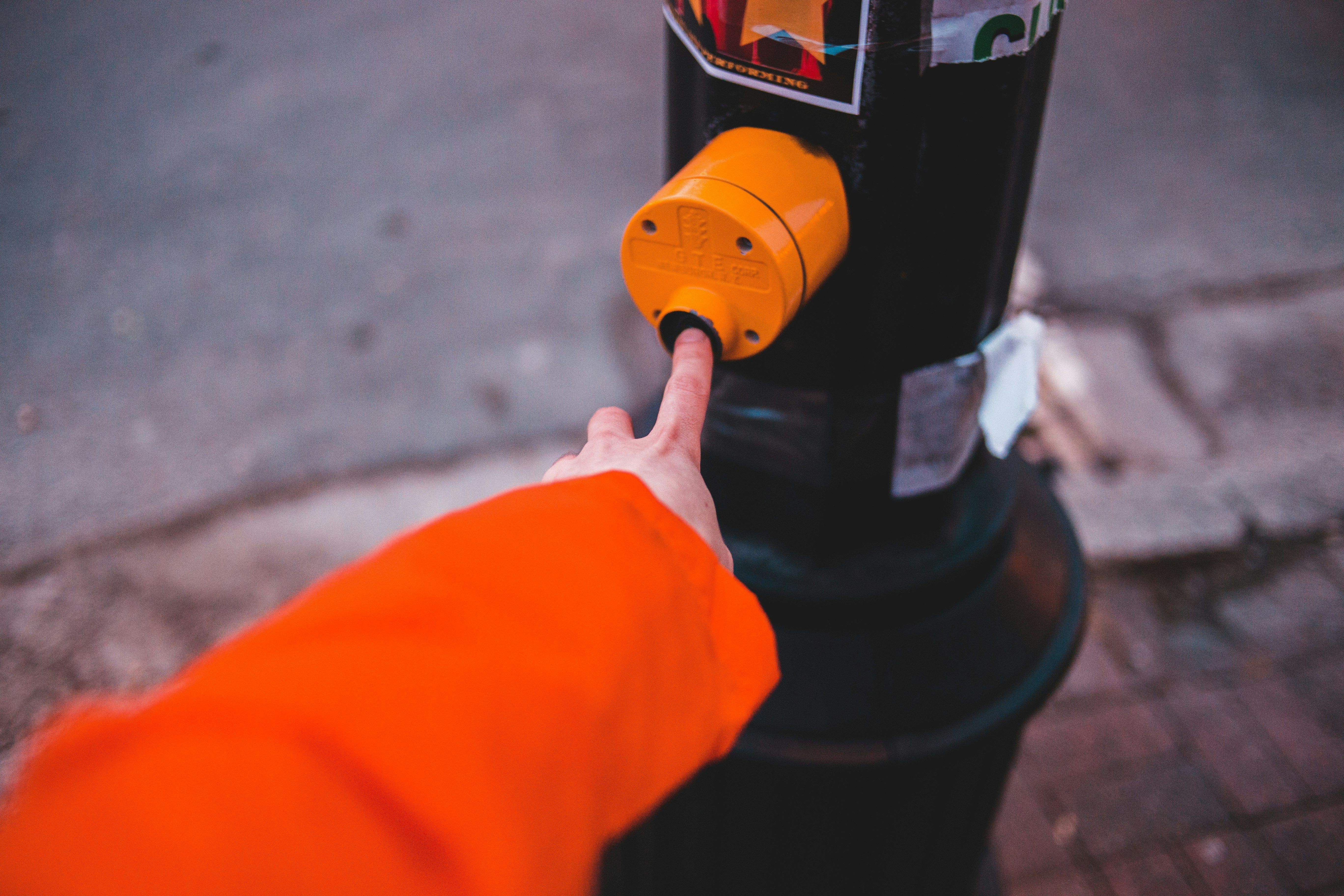 Push to Power: Hand on the Orange Cap at a Street Corner Post
