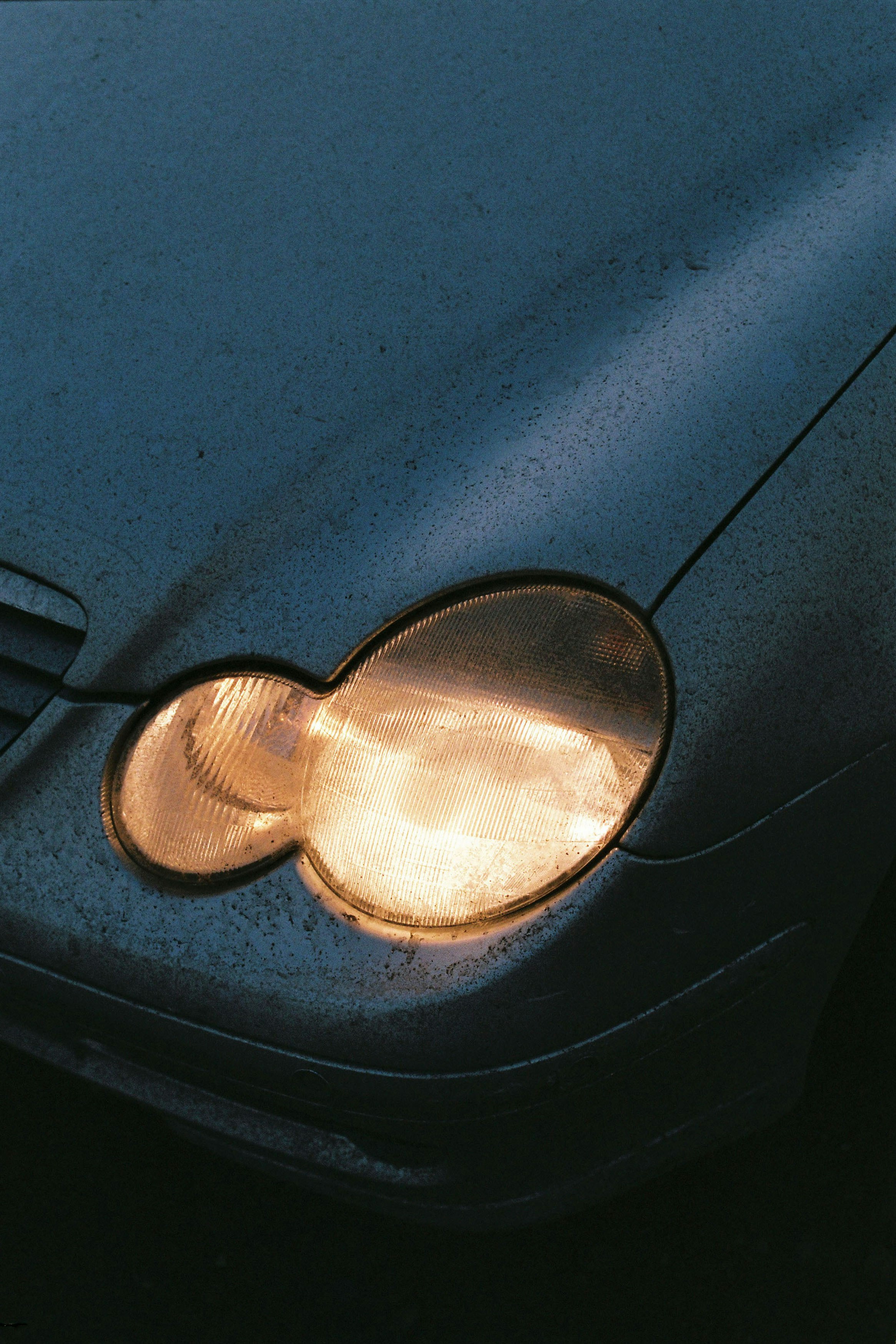 Close-up of a car's headlight with a soft glow, showcasing the intricate design and weathered surface. The scene evokes a sense of nostalgia.