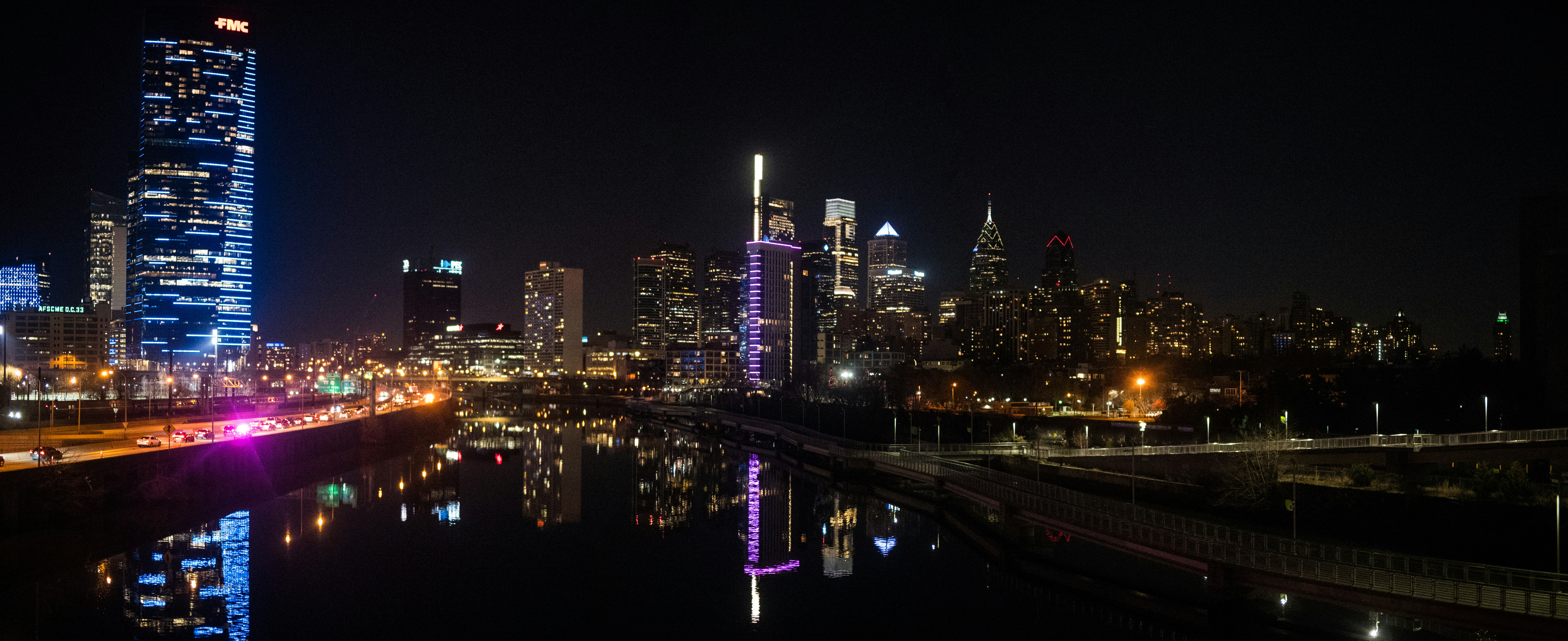 City skyline illuminated at night, with vibrant lights reflecting on the water. Skyscrapers create a dynamic urban landscape.