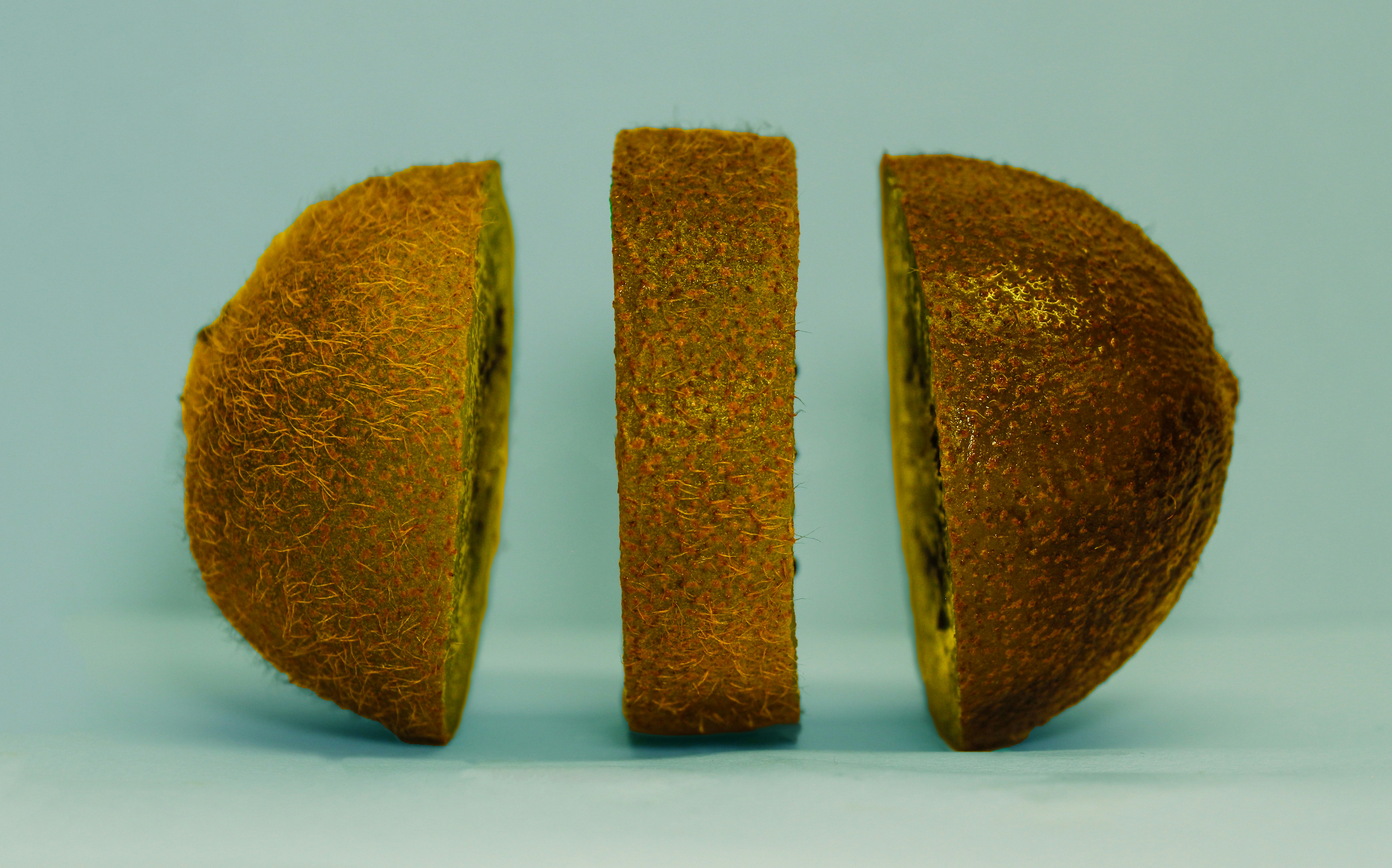 Three halves of a kiwi fruit showcasing its unique texture and vibrant interior against a soft blue background.