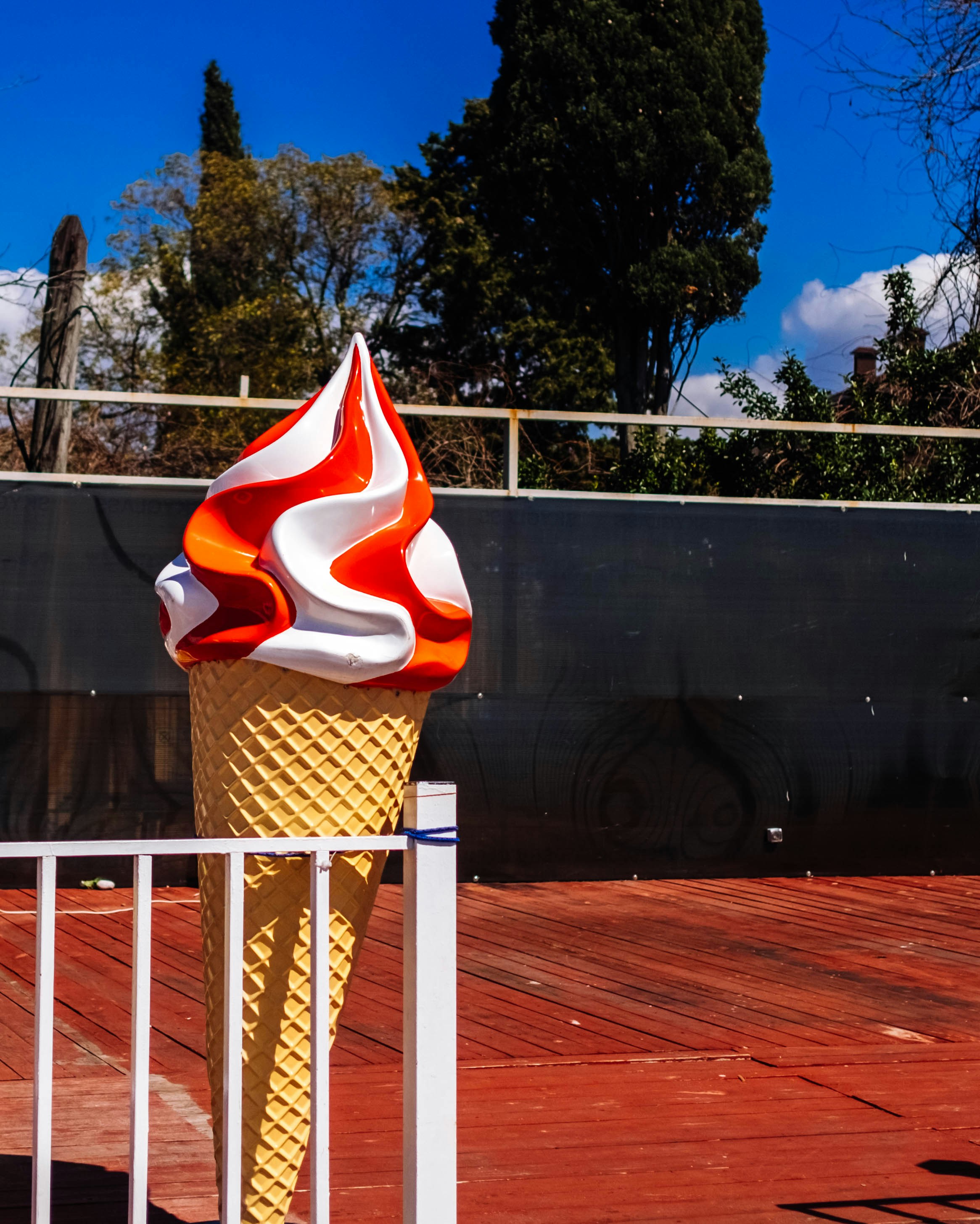 Sunlit Sentinel: A Giant Red-and-White Ice Cream Cone on a Boardwalk