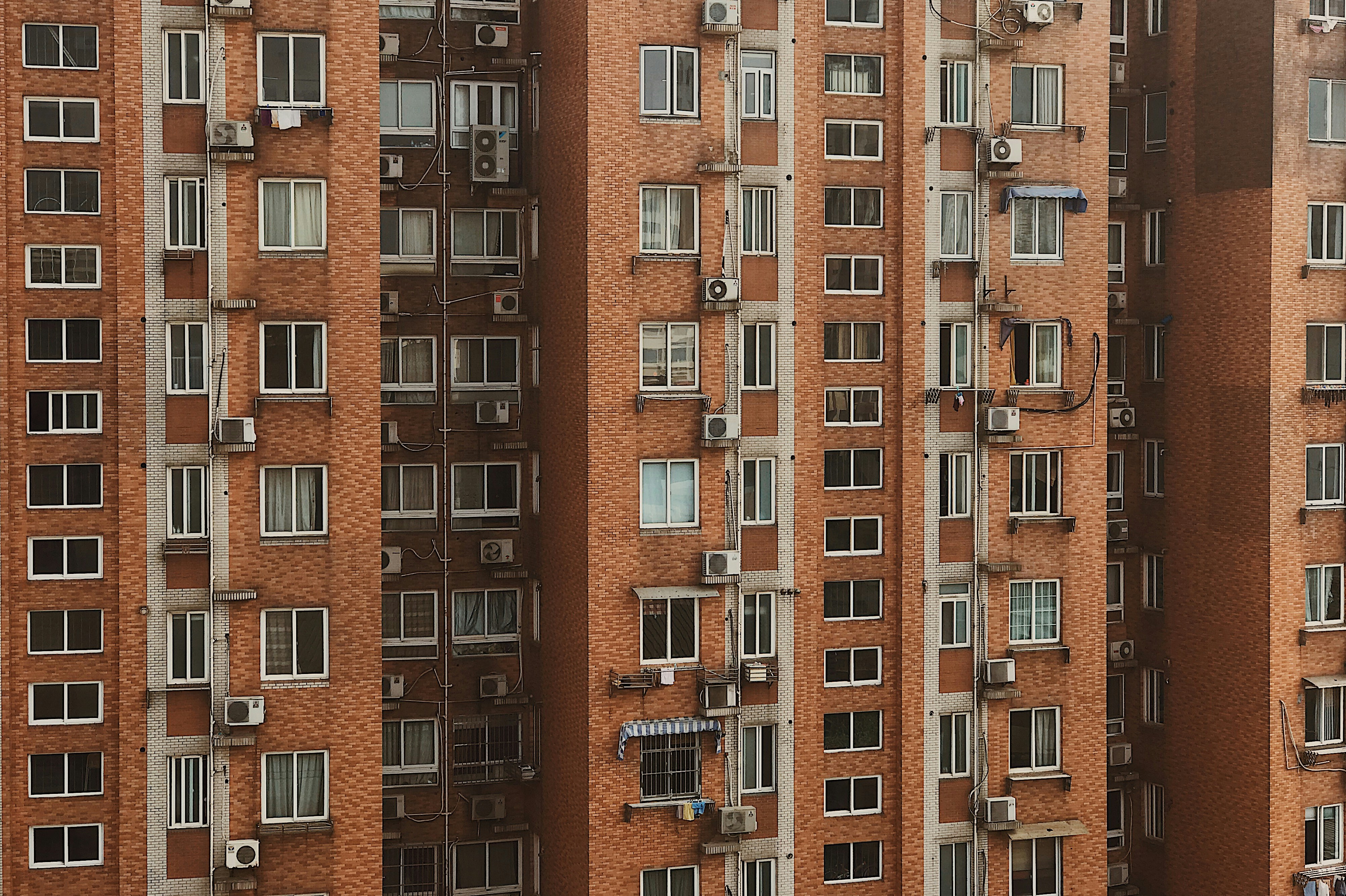 Close-up of a brick apartment building facade showcasing a pattern of windows and air conditioning units.