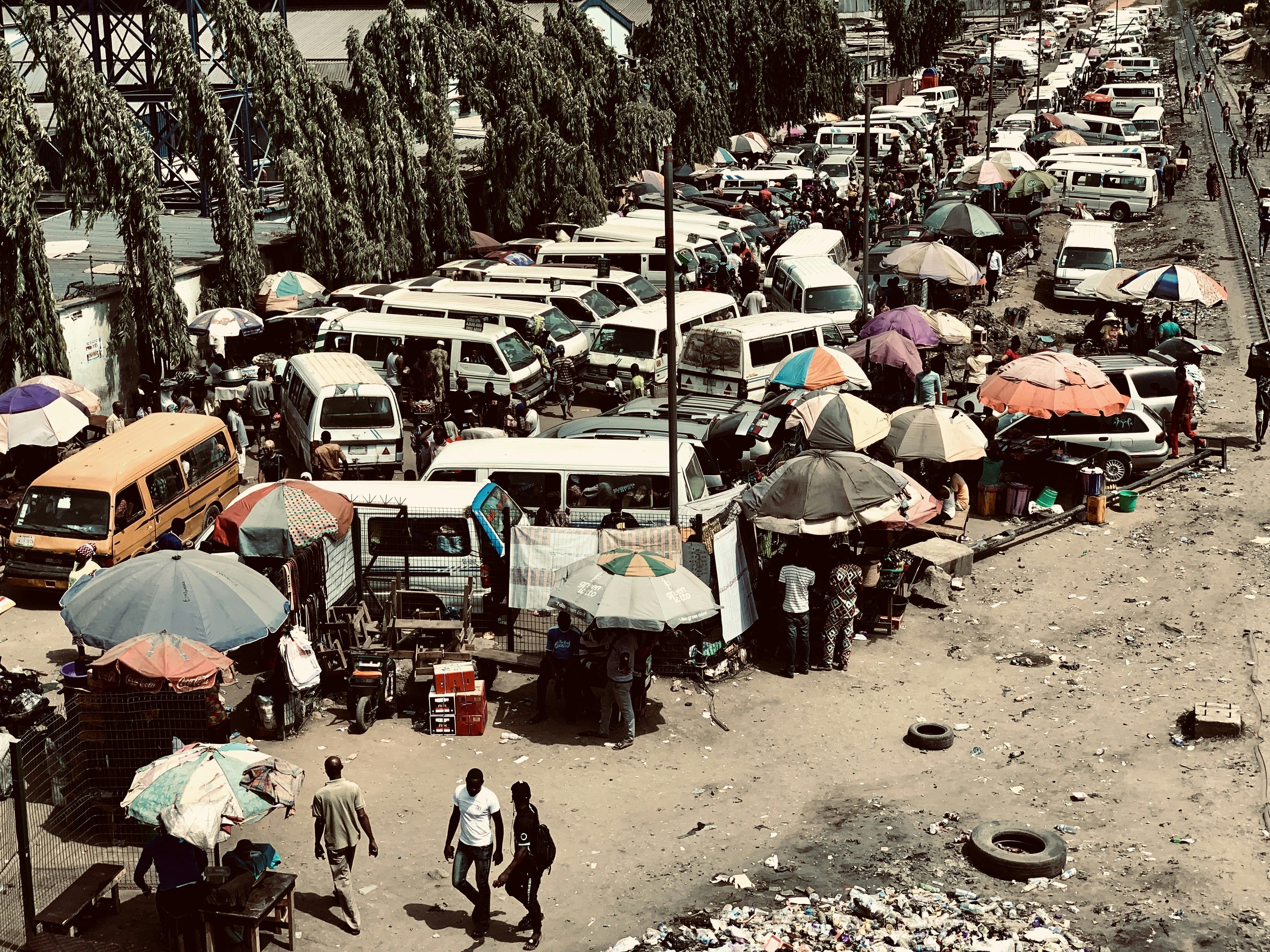 Aerial view of a crowded market with colorful umbrellas shading vendors and parked vehicles in a lively setting.