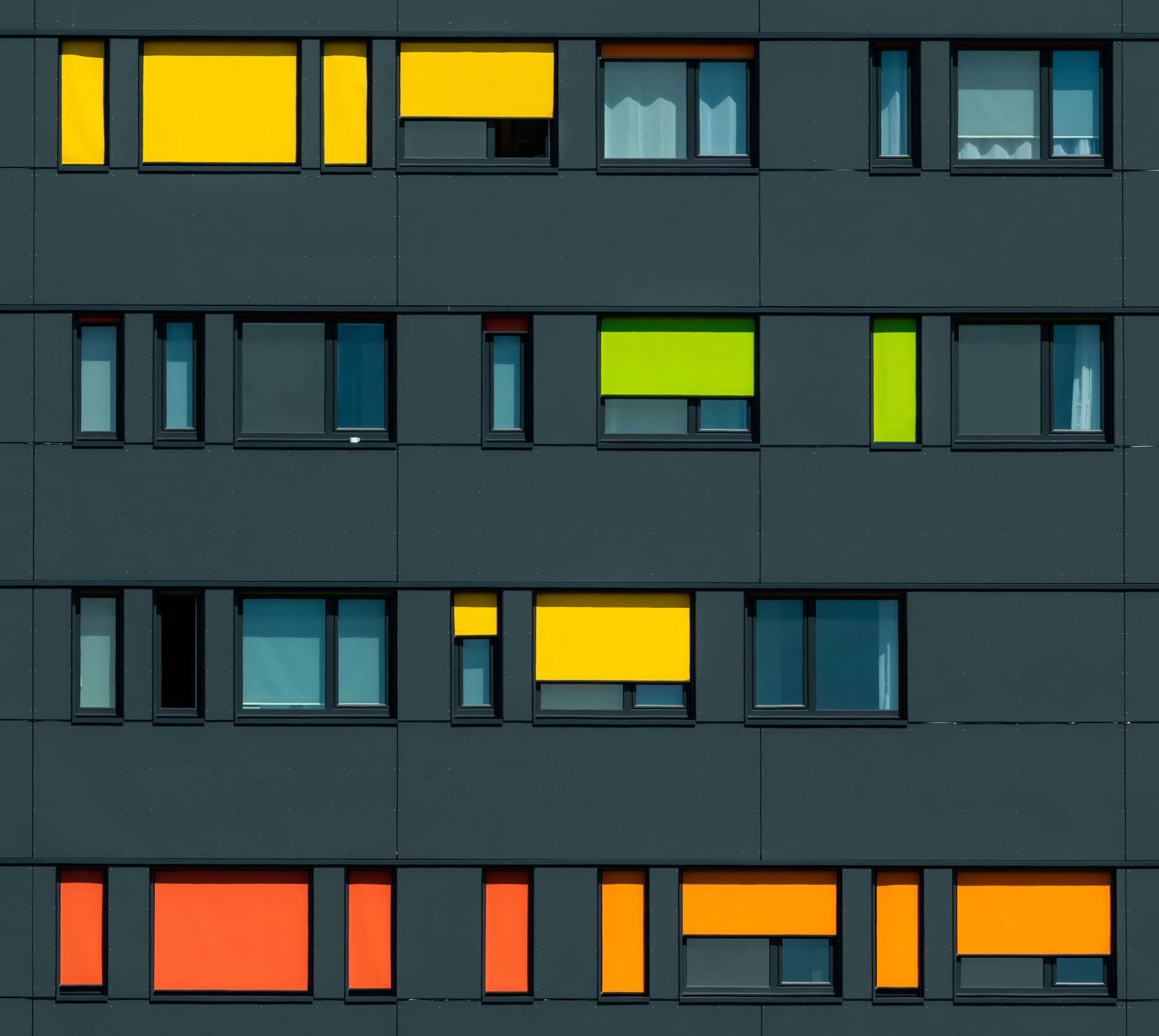 A modern building facade featuring a pattern of colorful windows in yellow, green, orange, and red against a dark background.