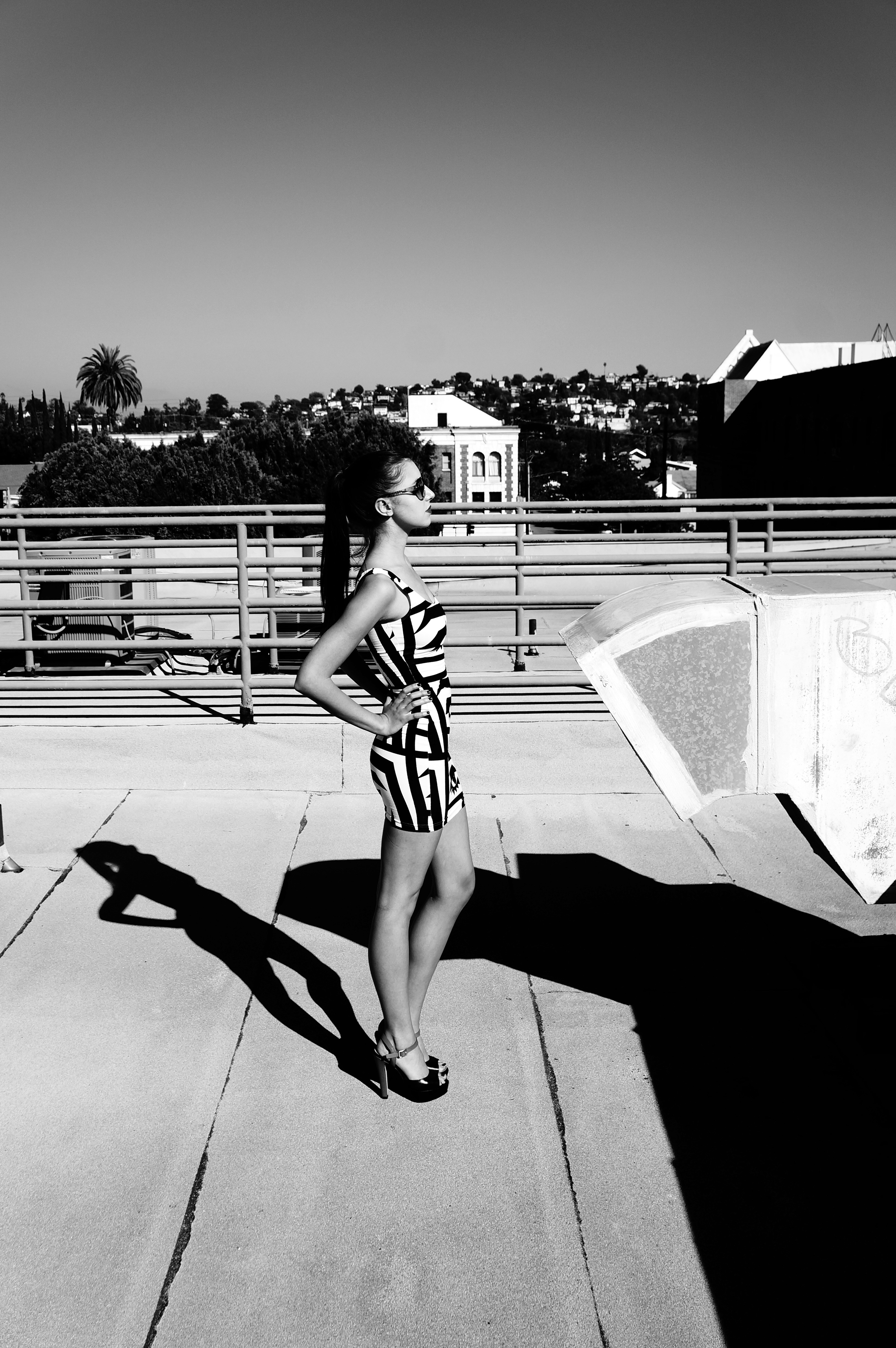 Woman in a striped dress stands confidently on a rooftop, casting a sharp shadow in the afternoon sun.