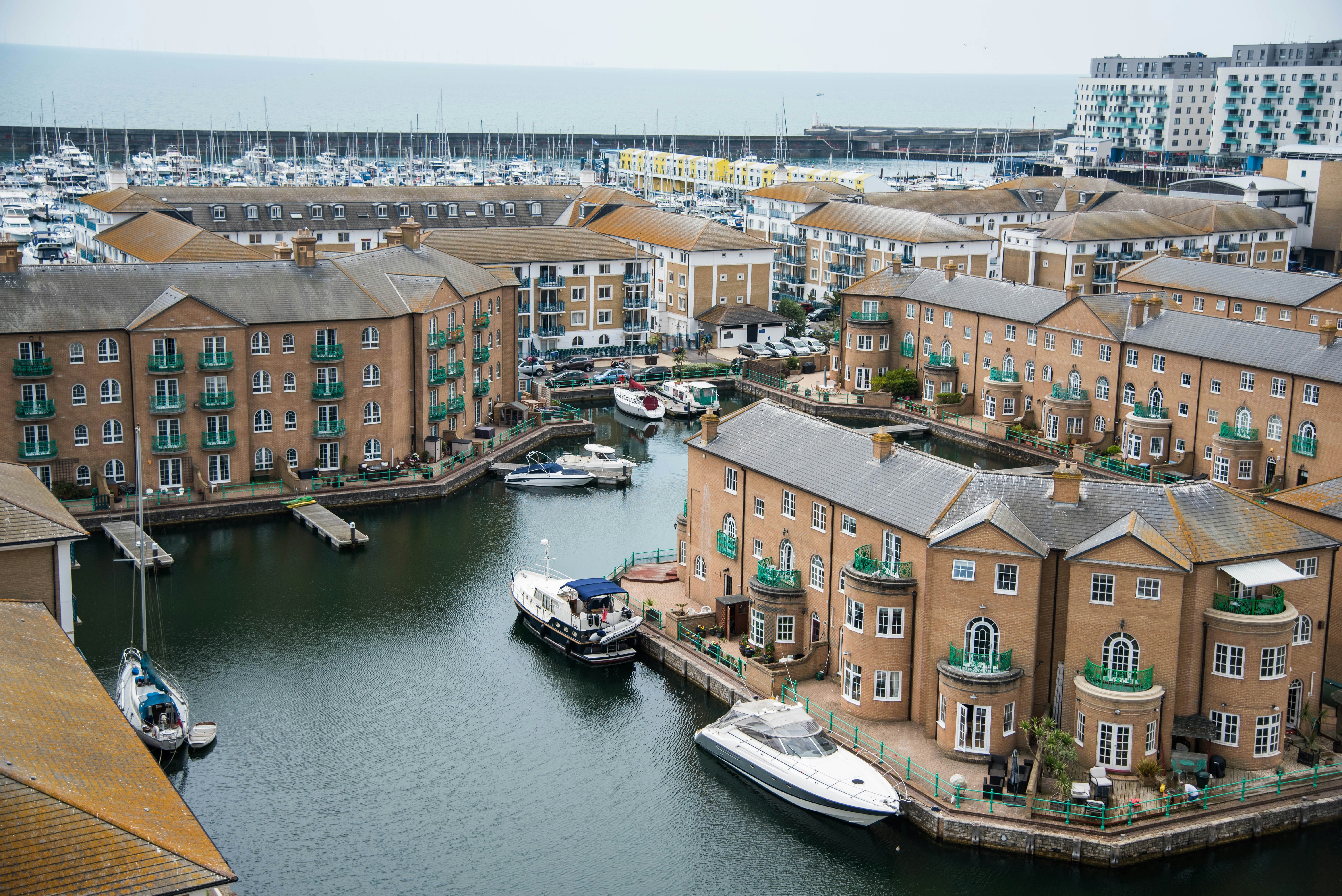 Brick waterfront homes encircle a marina filled with yachts under a cloudy sky.
