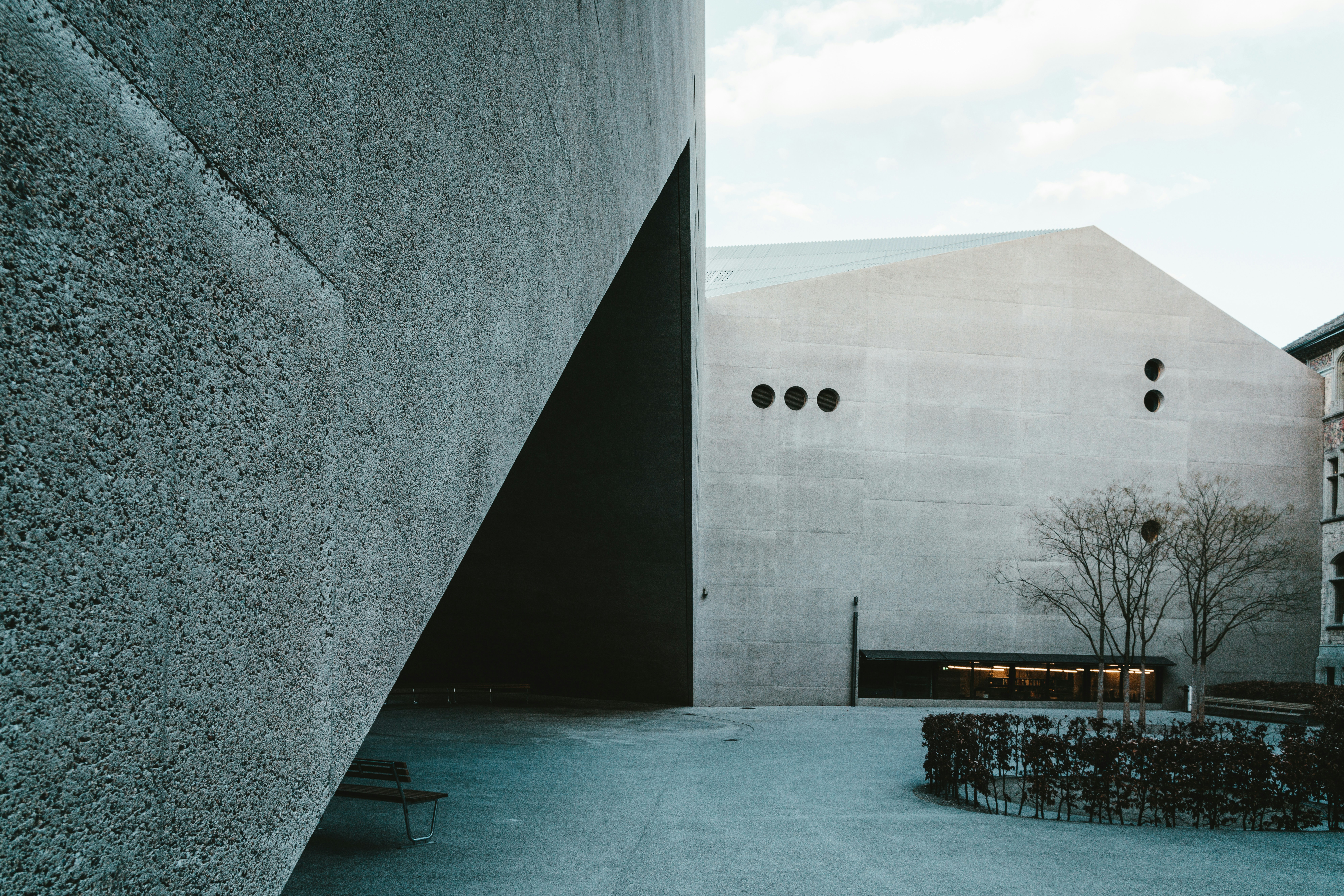 Abstract architectural composition featuring angular concrete structures and a solitary tree in a minimalist courtyard.