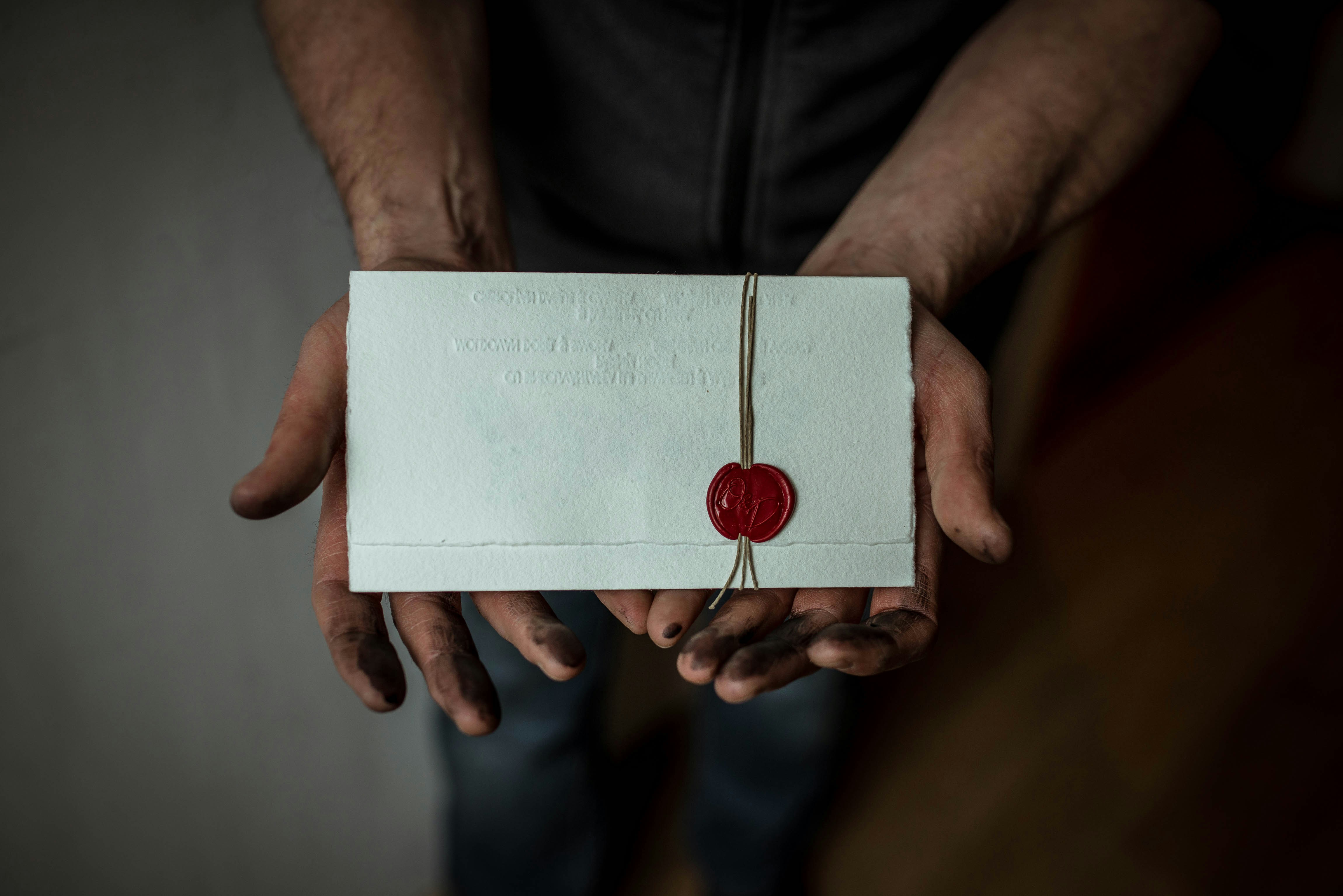 Hands presenting a sealed envelope with a red wax seal, hinting at a hidden message inside. The textured paper contrasts with the worn hands, suggesting a story waiting to be unveiled.