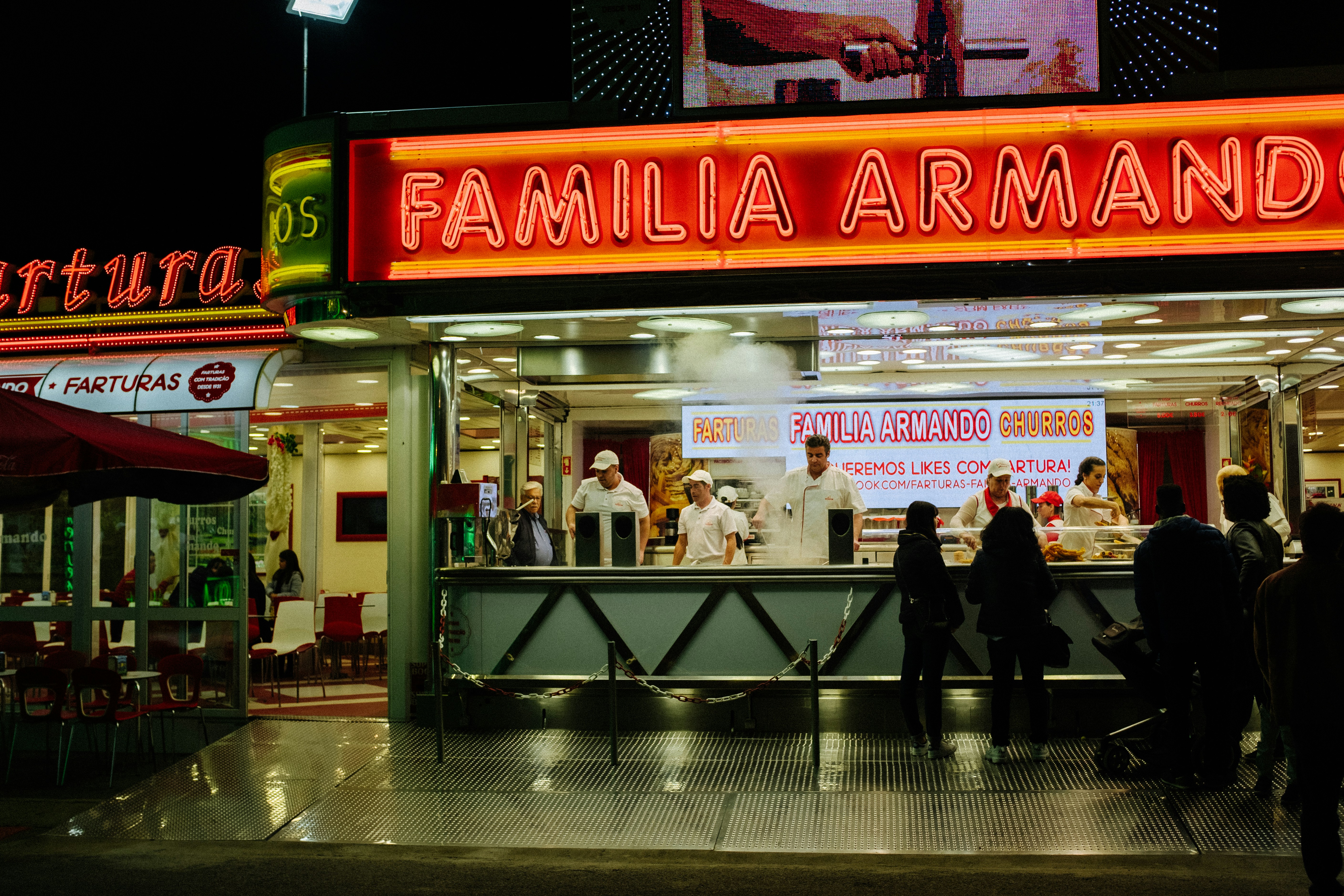 Vibrant food stall illuminated by neon lights, showcasing chefs preparing dishes in a bustling night market atmosphere.
