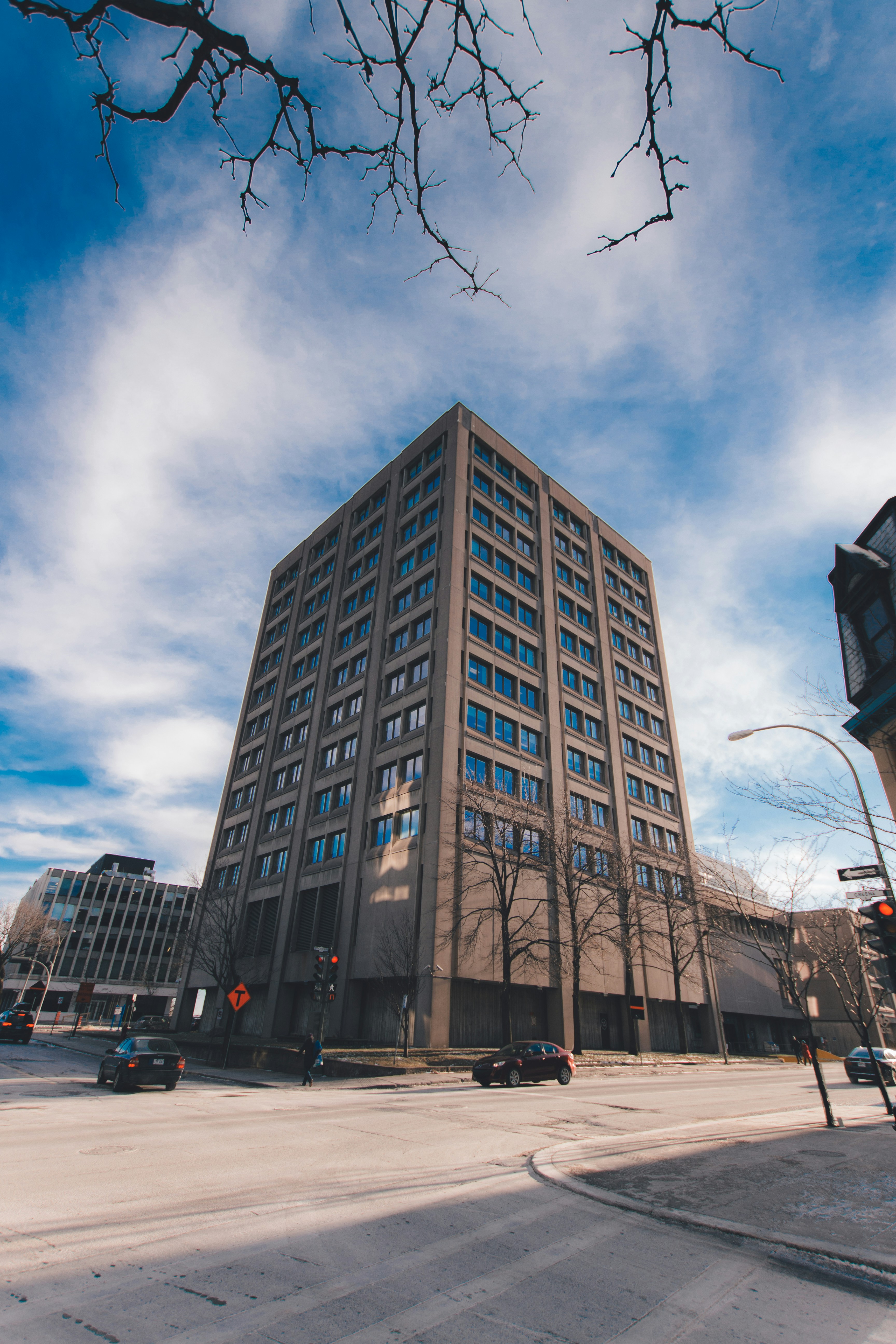 A tall, modern building with a grid-like facade stands prominently at an urban intersection, framed by a clear blue sky and wispy clouds.