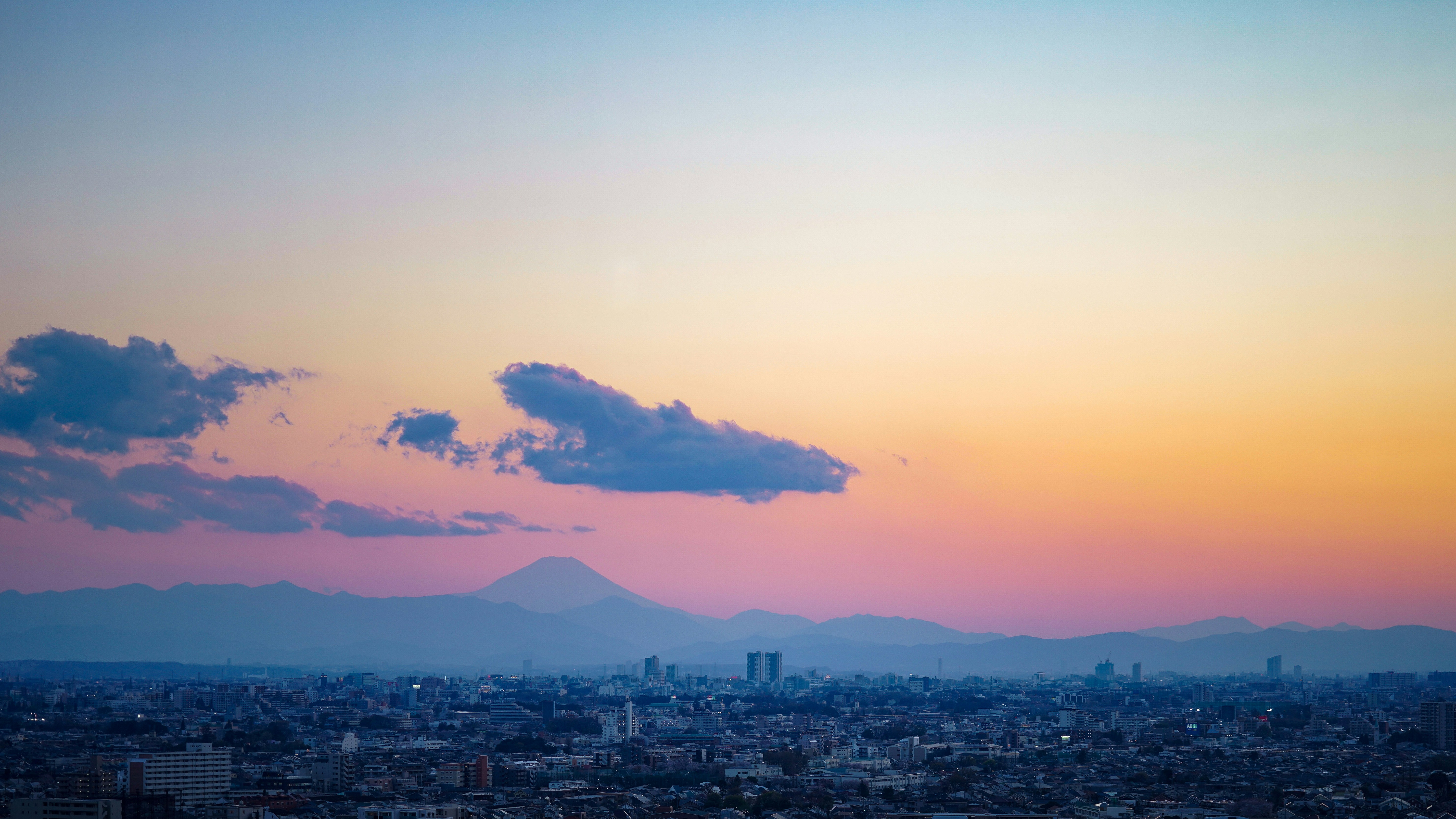 Expansive city skyline beneath a colorful sunset with distant mountains and scattered clouds.