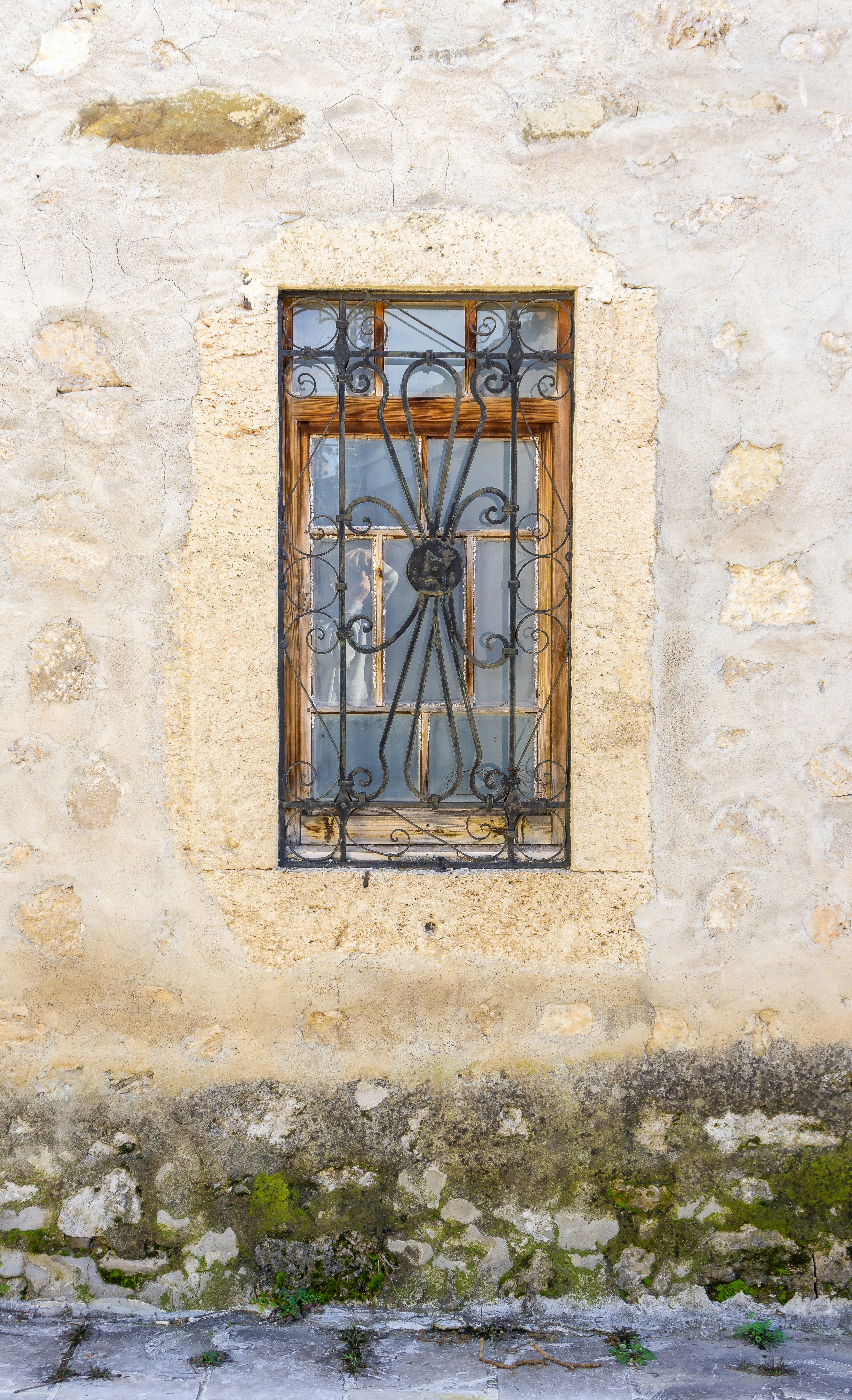 A rustic wooden window framed by intricate wrought iron grilles set against a weathered stone wall, showcasing the charm of aged architecture.