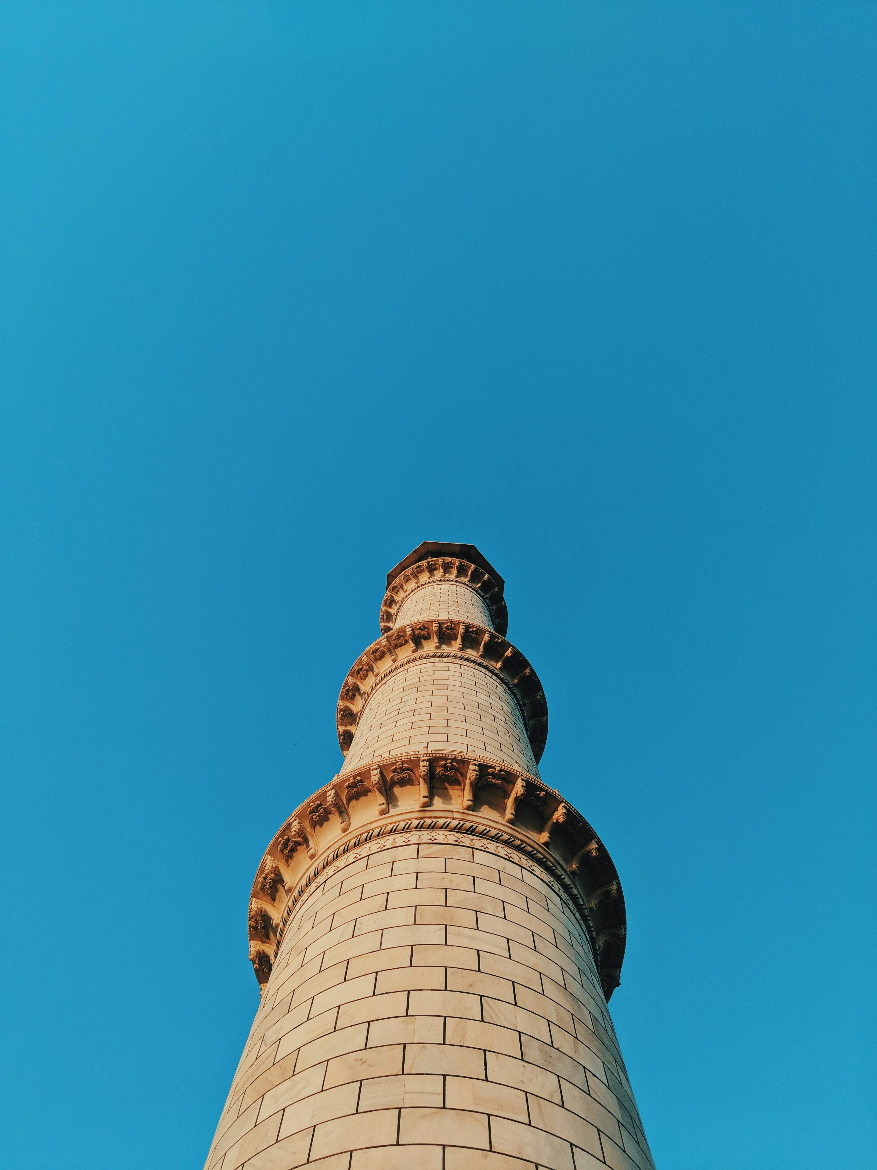 A towering minaret rises against a clear blue sky, showcasing intricate architectural details. The perspective emphasizes its grandeur and height.