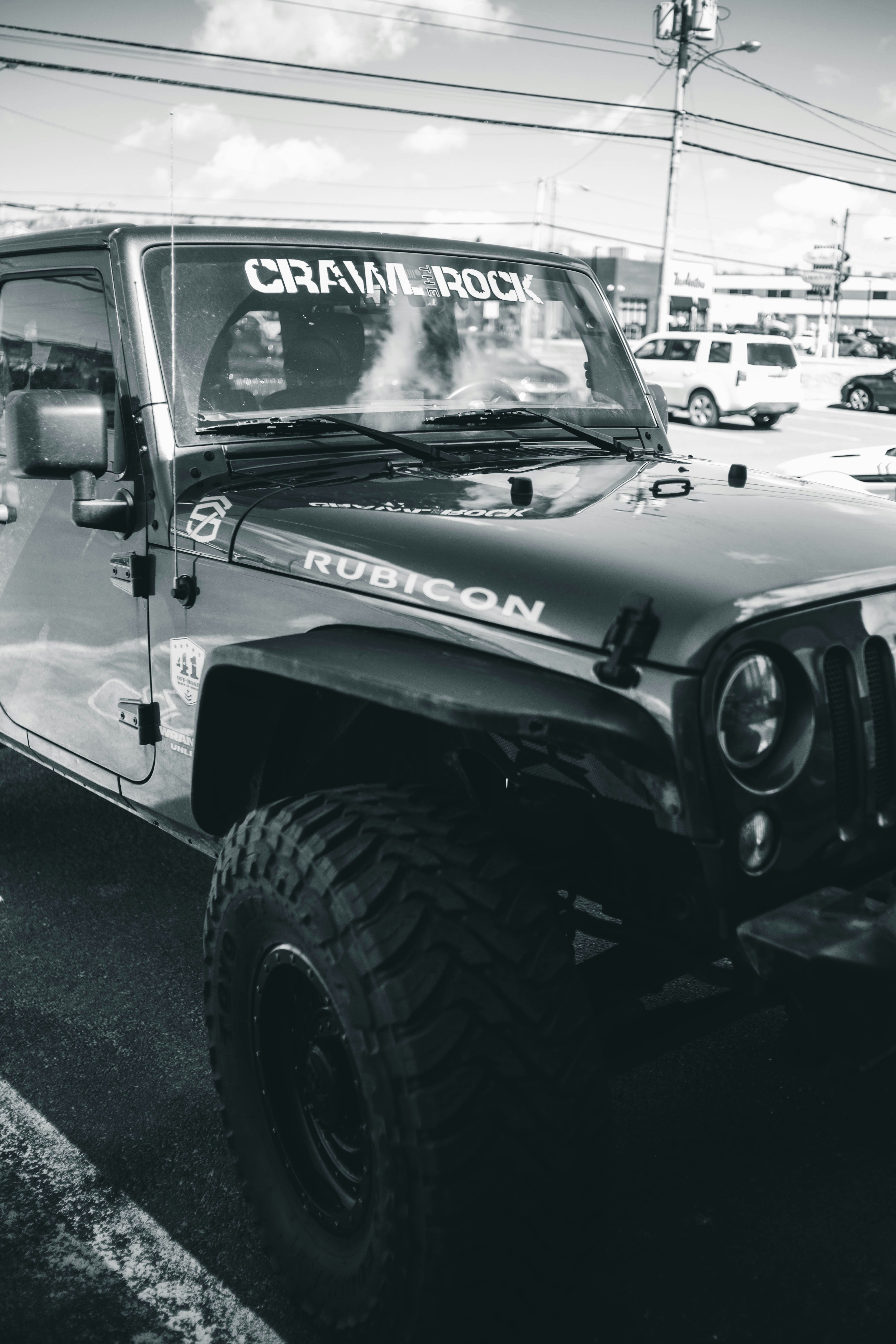 Grayscale Rubicon: rugged Jeep beneath an urban power-line grid
