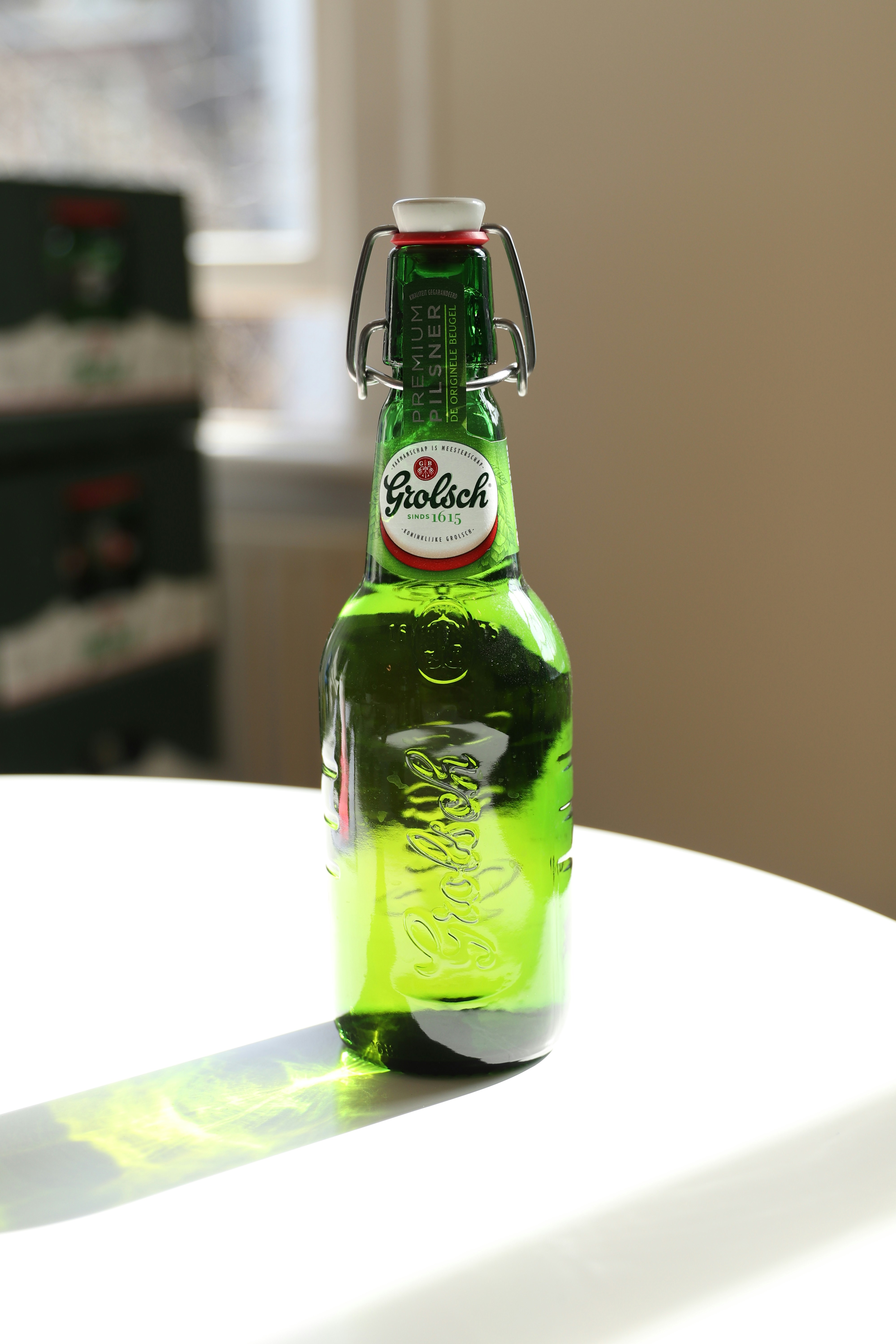 Green Grolsch beer bottle with distinctive swing-top cap reflecting sunlight on a white surface.
