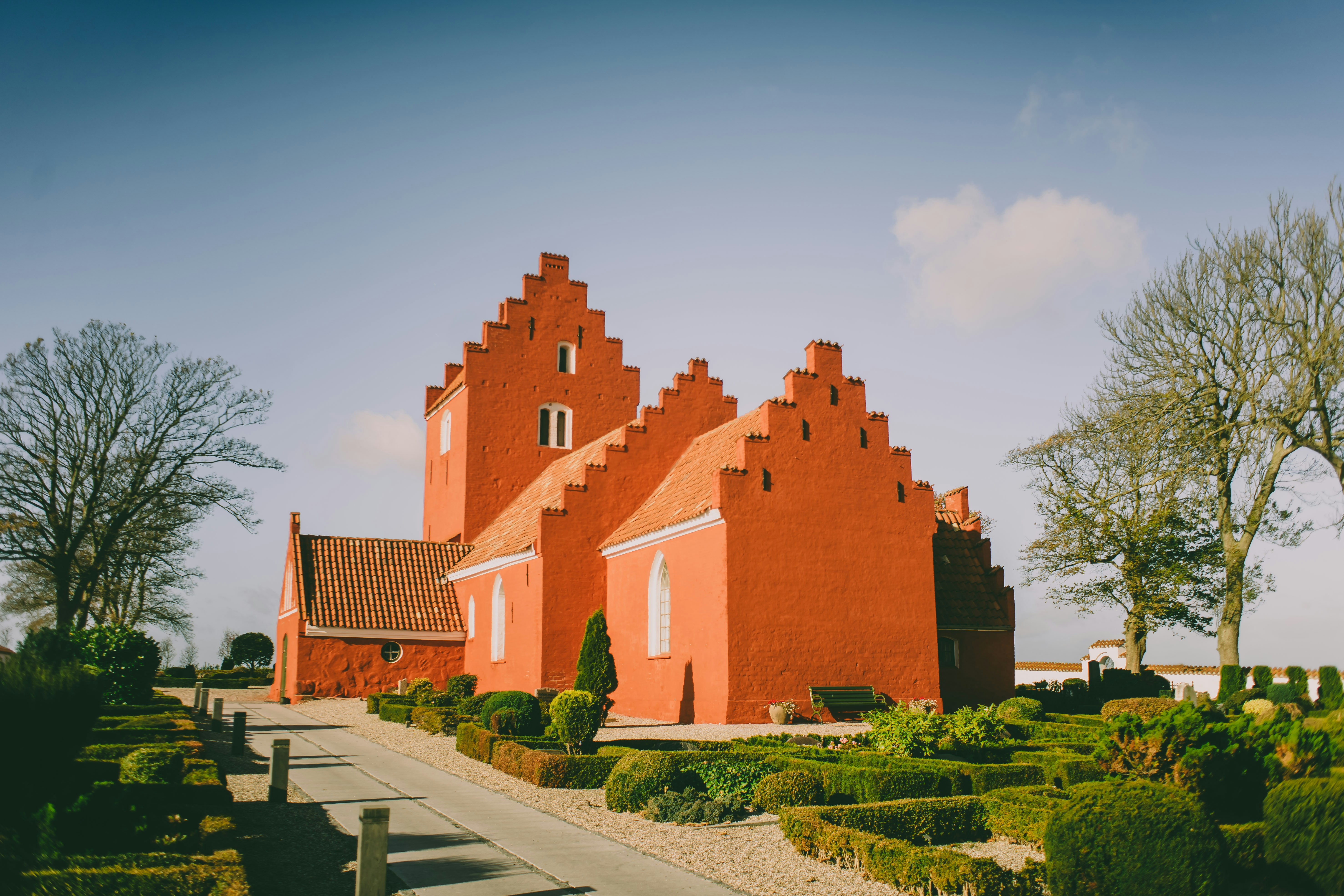 Distinctive red brick building with stair-step gables surrounded by manicured hedges under a clear blue sky.