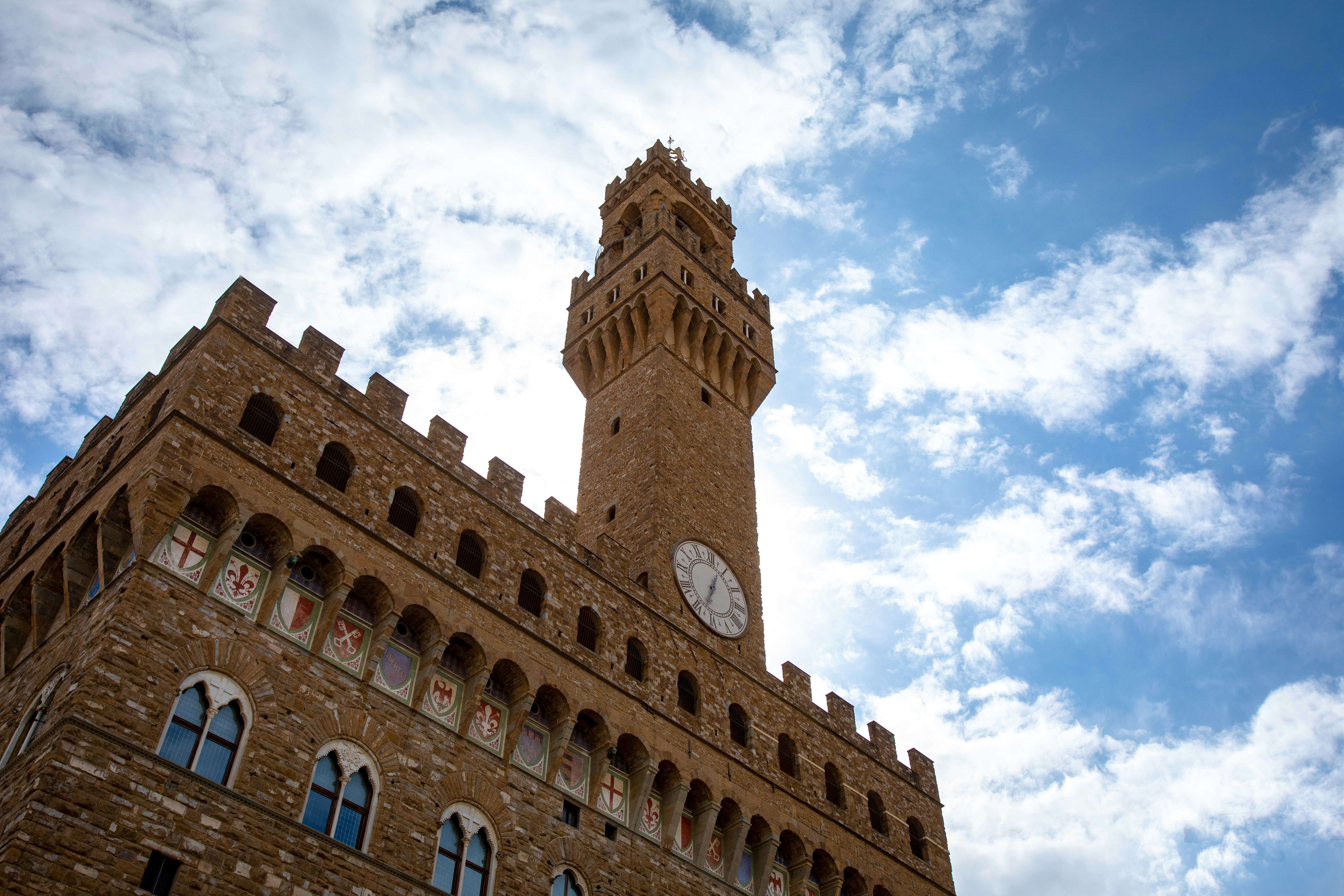 Historic stone tower with clock under a partly cloudy blue sky.