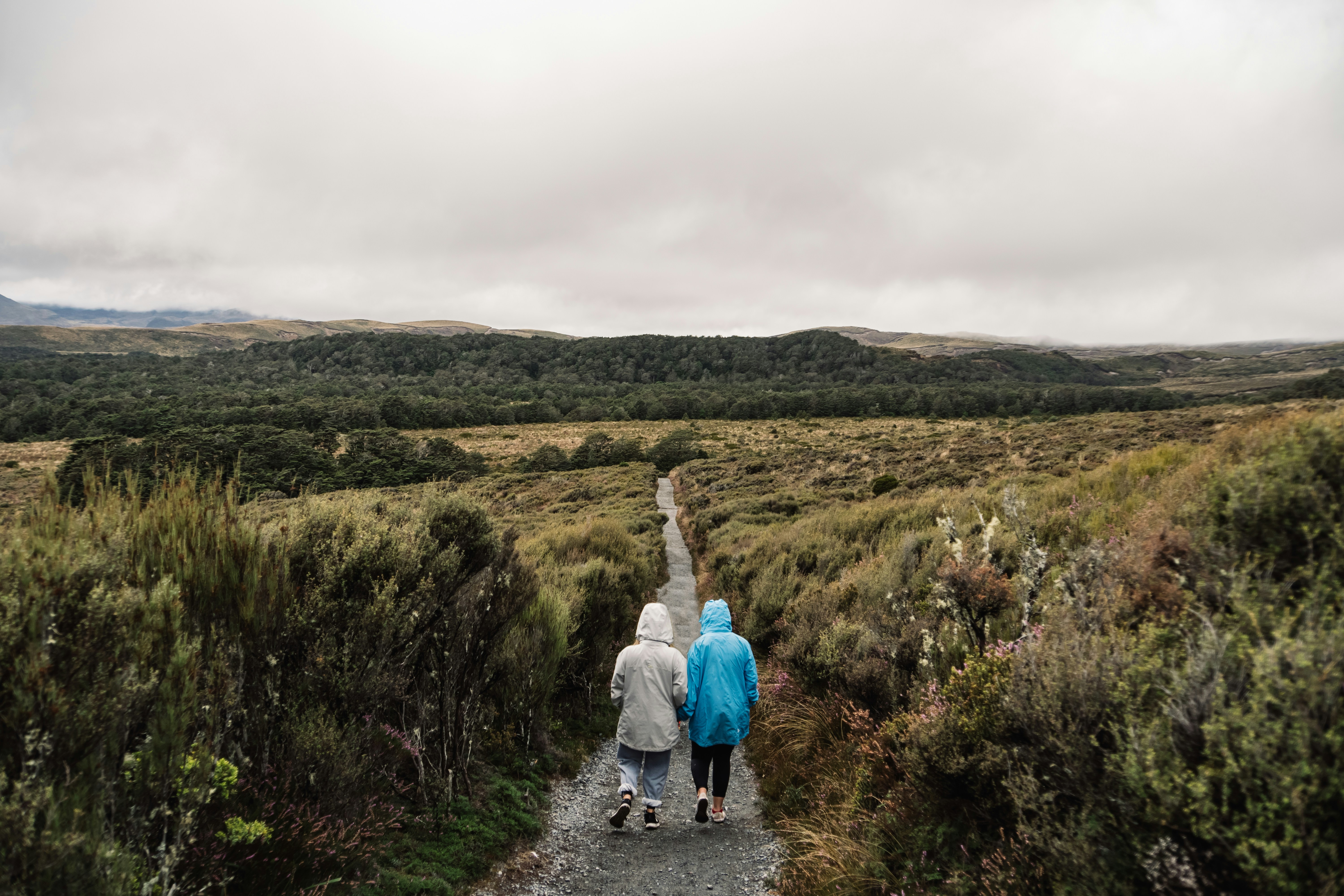 Grey Moor Crossing: Two Hikers Trace a Narrow Gravel Path Under Leaden Skies