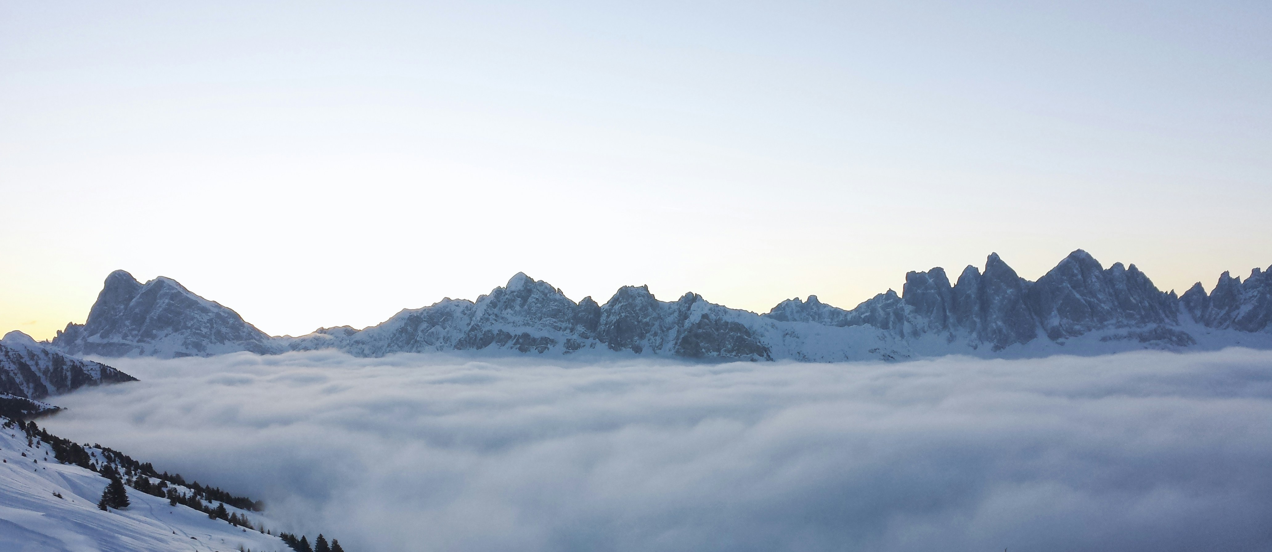Snow-covered mountains rising above a sea of clouds at sunrise.