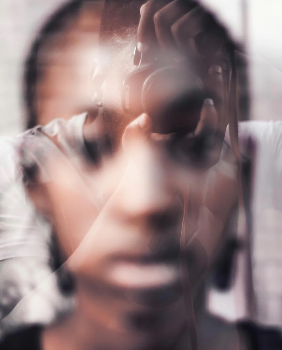 A softly blurred close-up of a person wearing headphones, with the camera held near the face and bright light flaring across the center. The portrait has a dreamy, reflective feel.