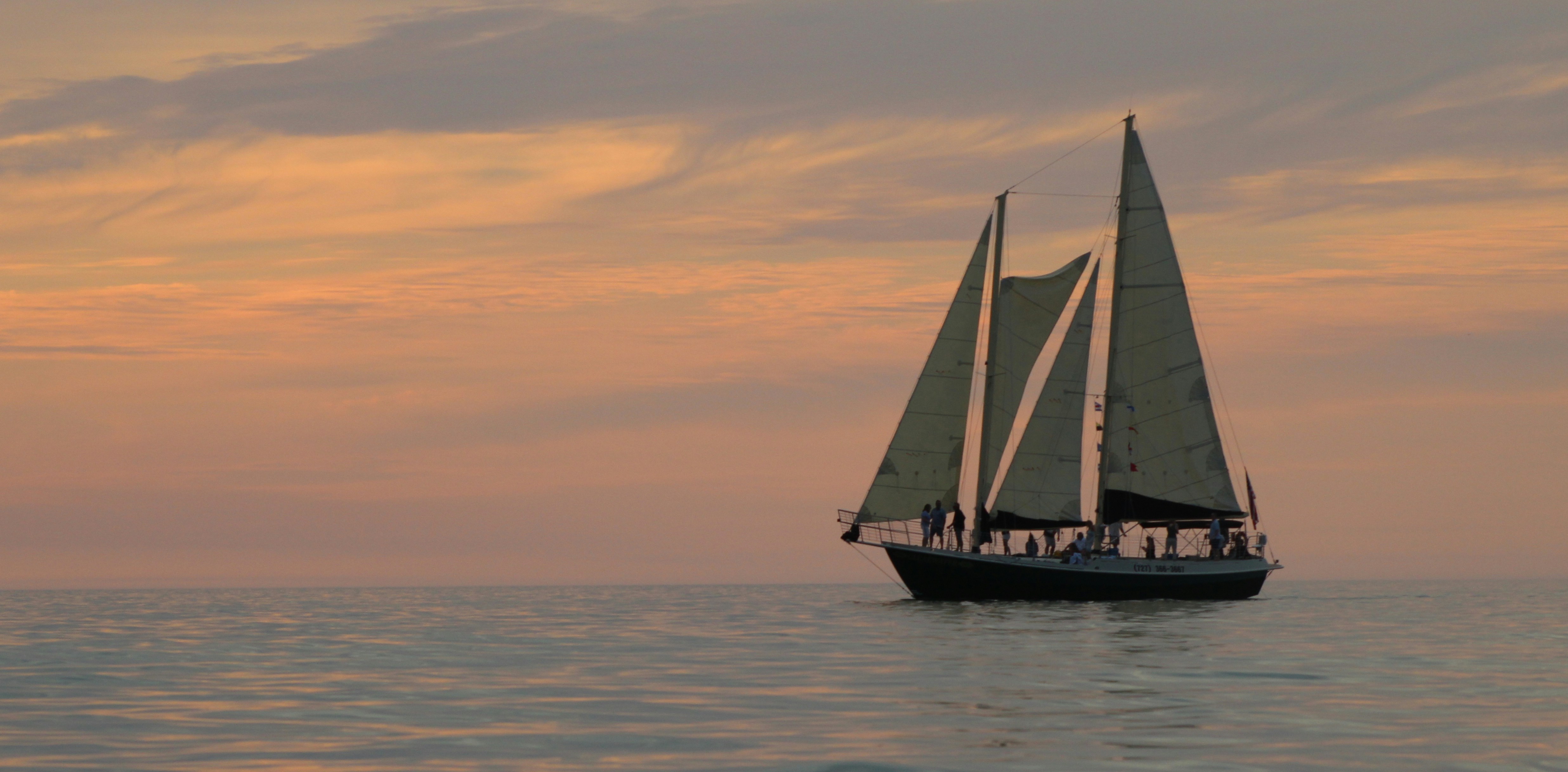 Sailboat gliding across calm sea under a pastel sunset sky.