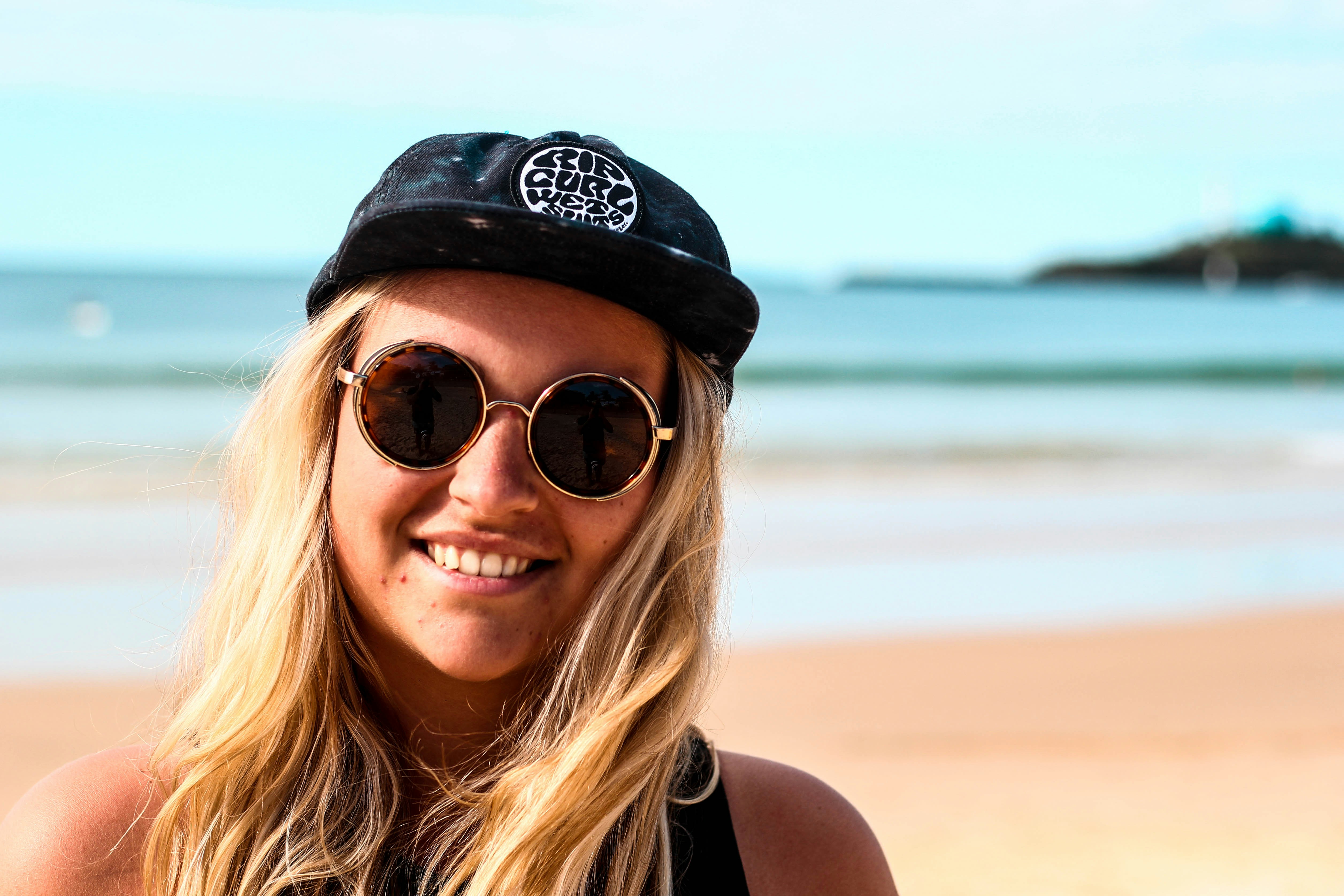 Sunlit Shore Portrait: Beachside smile with round sunglasses and a cap