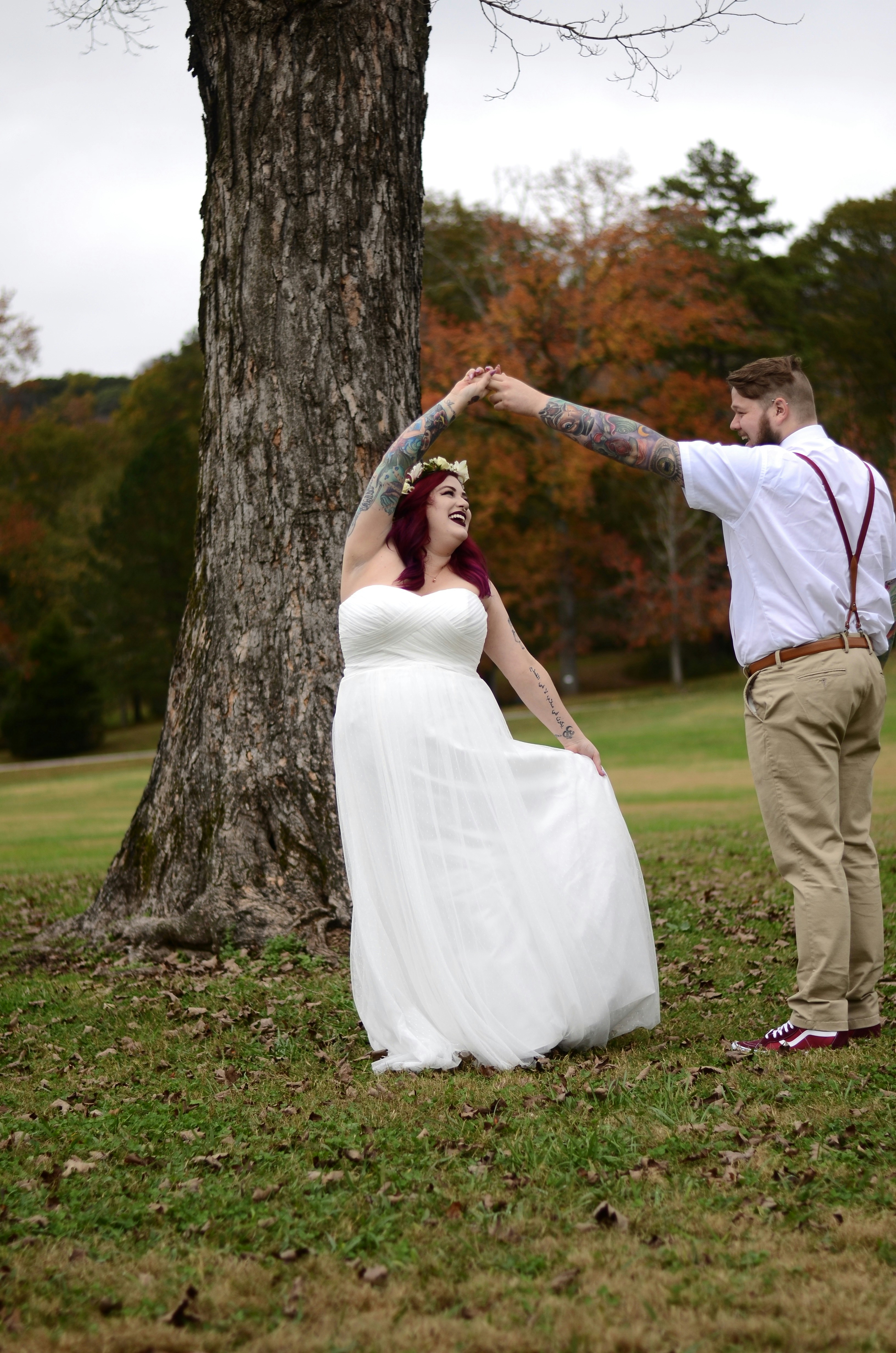 Couple joyfully dancing beneath a large tree, surrounded by vibrant autumn foliage. The scene captures a moment of celebration and love.