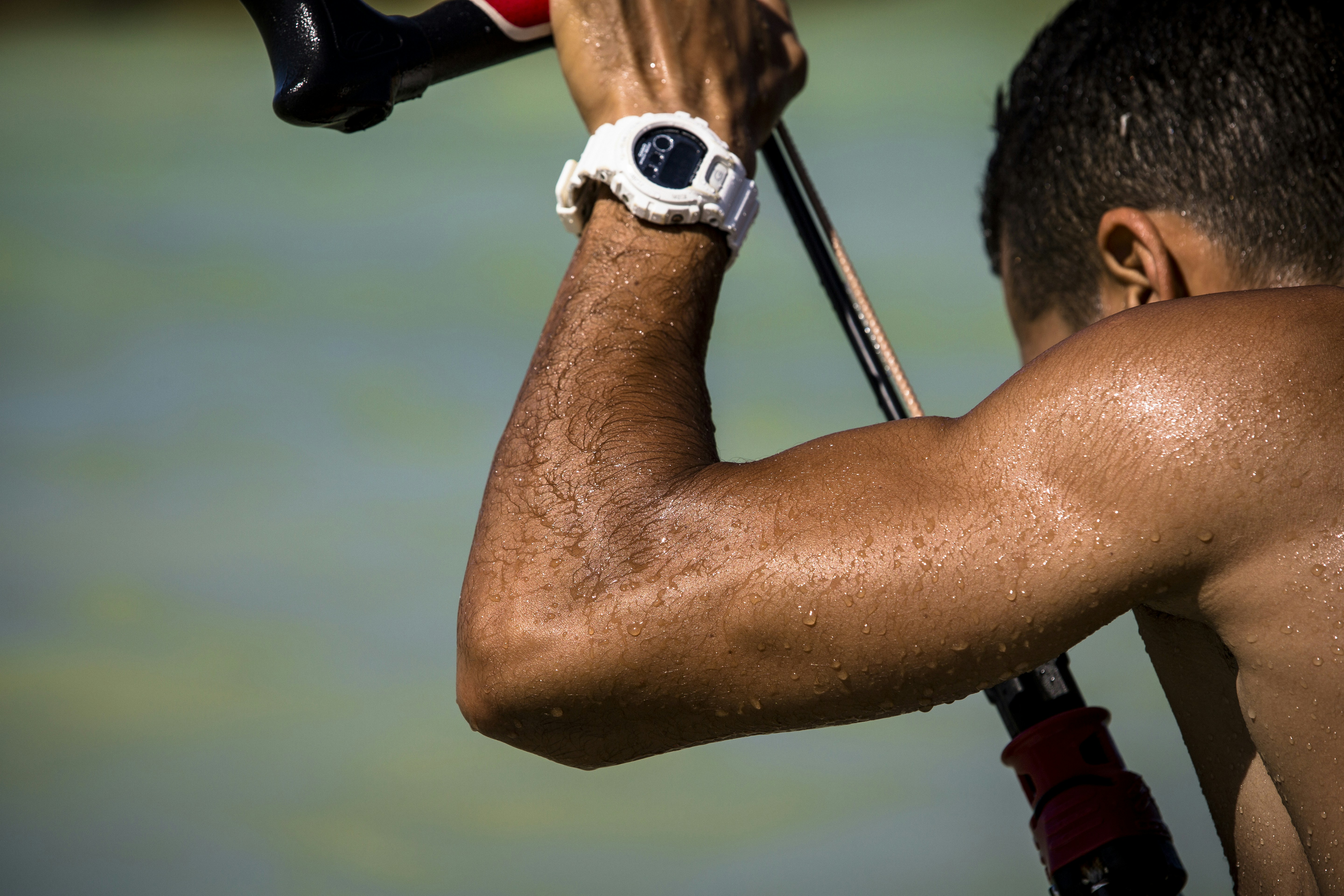 Close-up of a shirtless athlete gripping a paddle, wearing a white wristwatch against a blurred background.