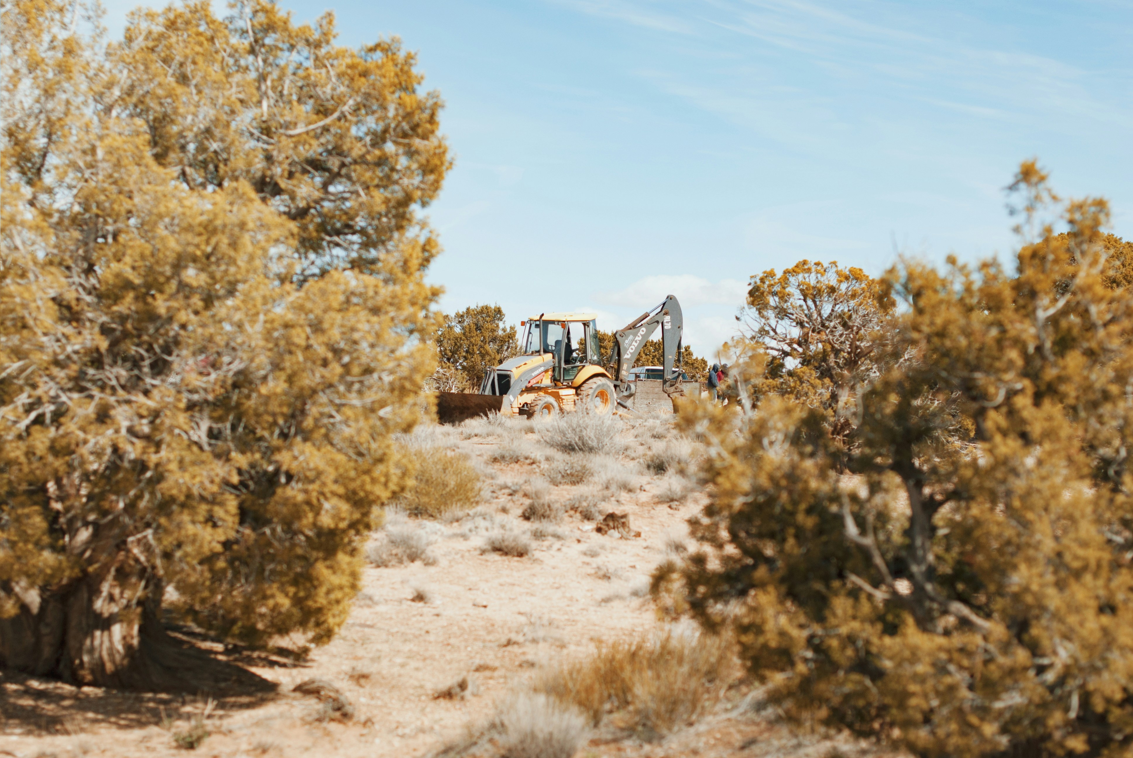 Heavy machinery working amidst rugged terrain and sparse vegetation under a clear blue sky.