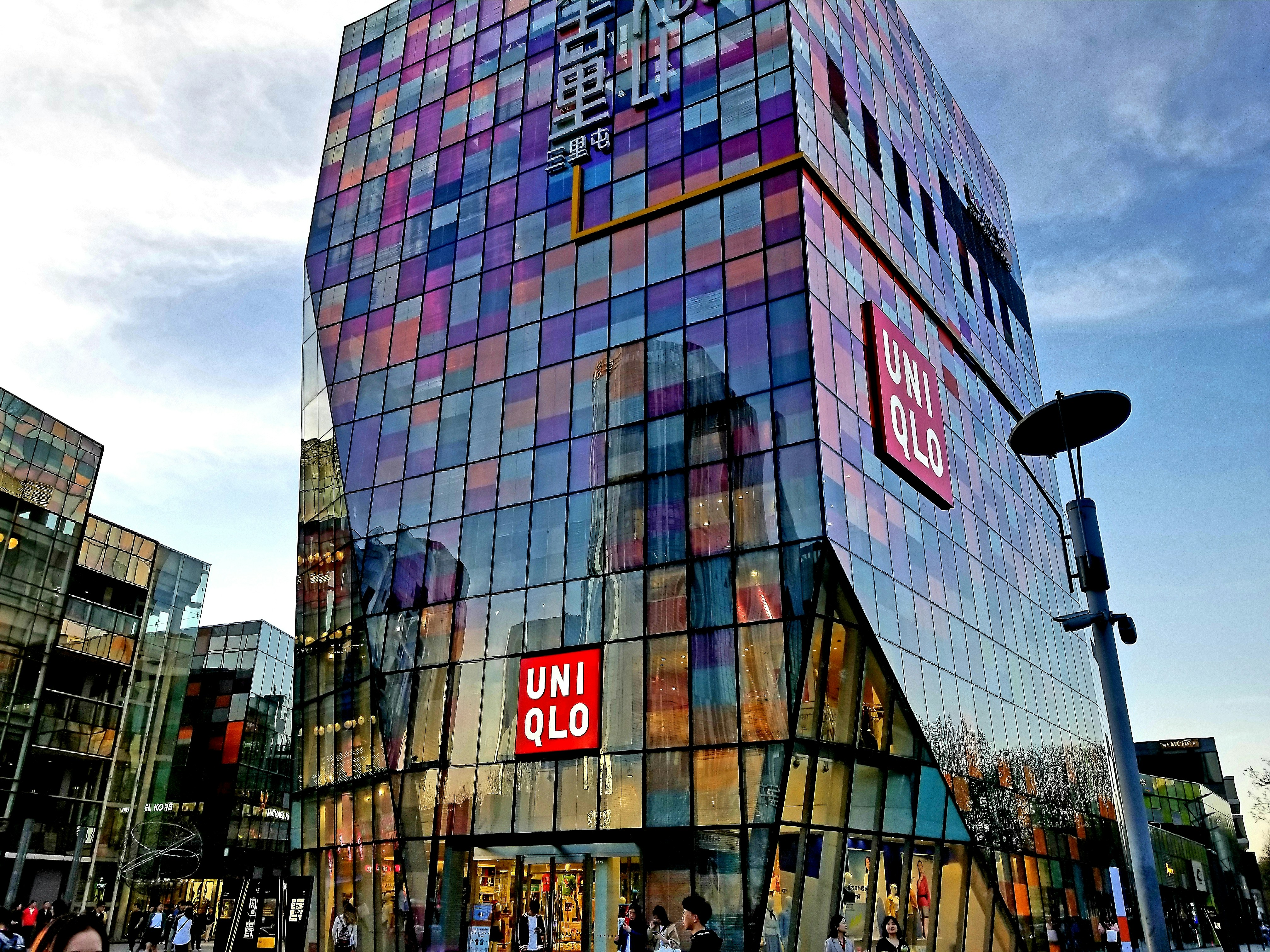 Colorful glass building with reflective panels under a vibrant sky.