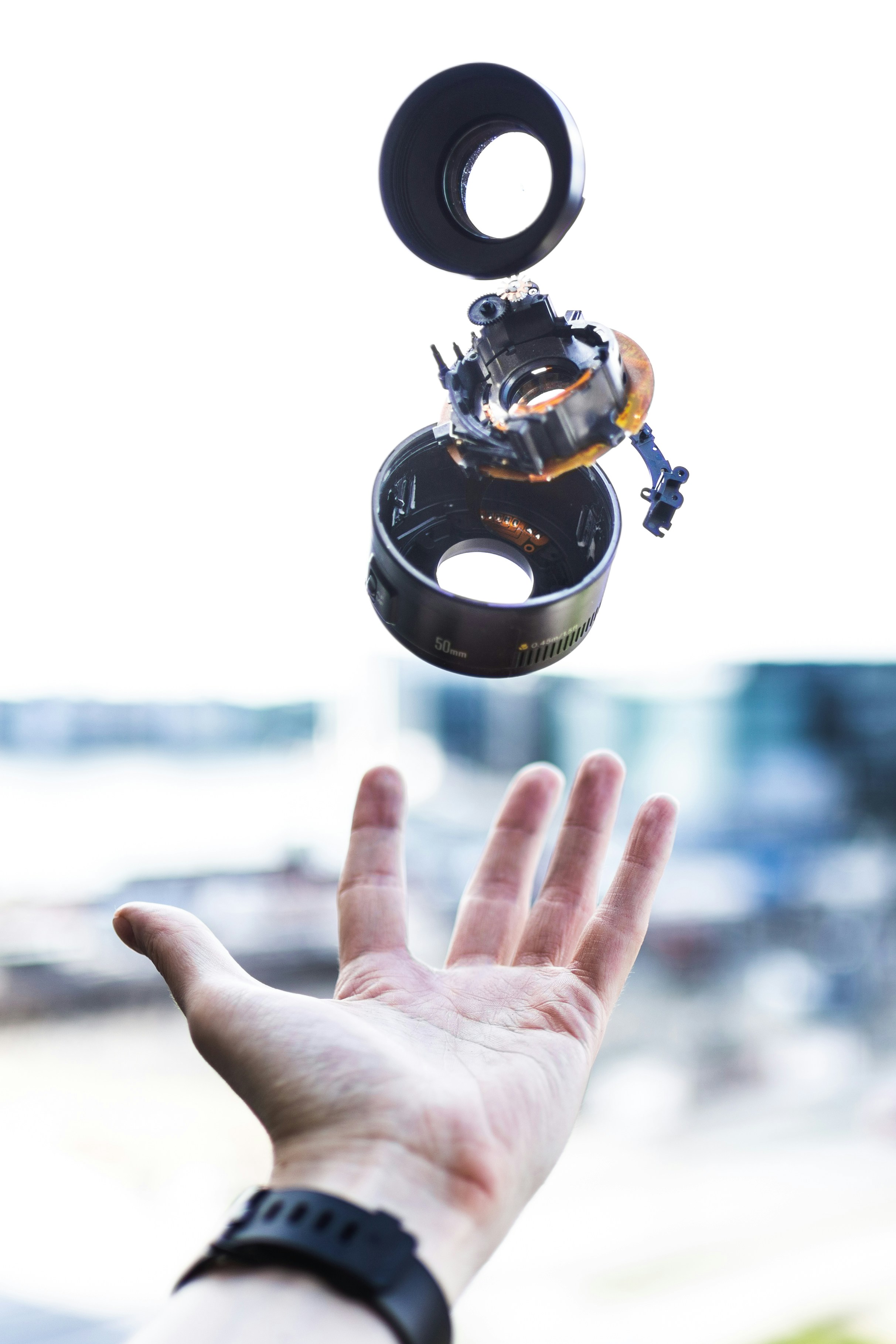 A hand reaches out as camera lens components float above, showcasing the intricate mechanics of photography equipment.