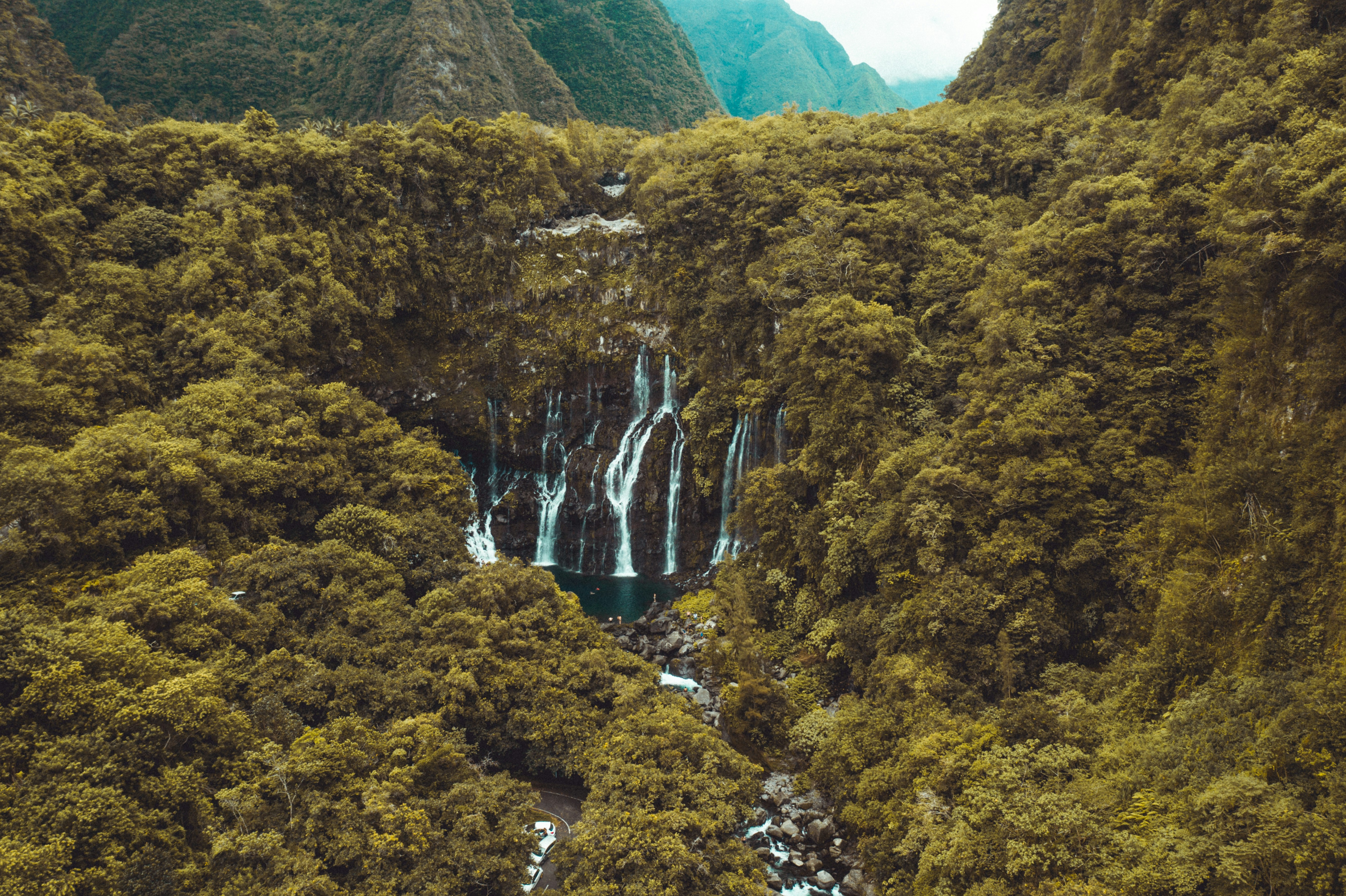 Waterfall streams through lush green mountains, surrounded by misty cliffs.