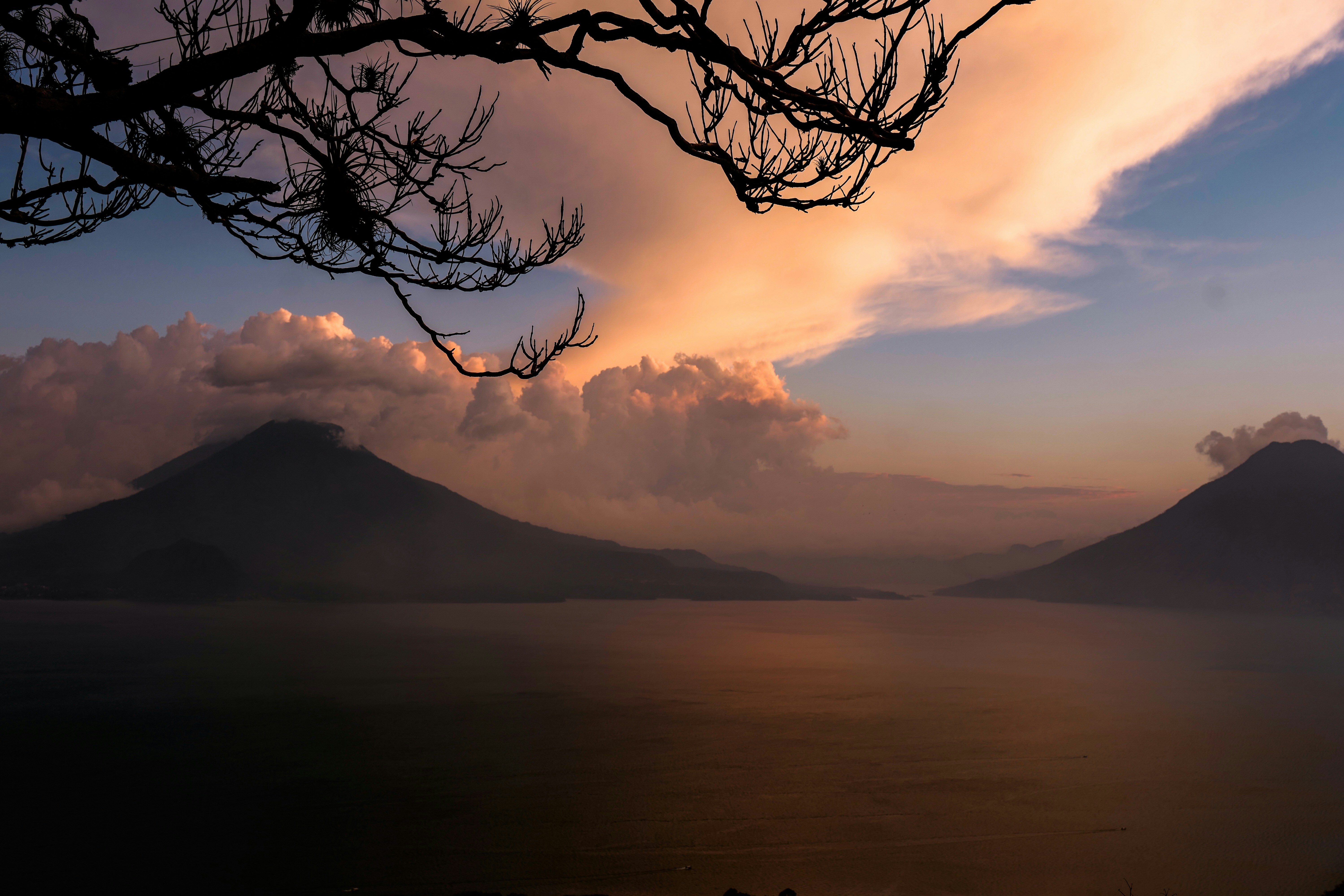Silhouetted volcanoes beneath dramatic, swirling clouds at sunset.