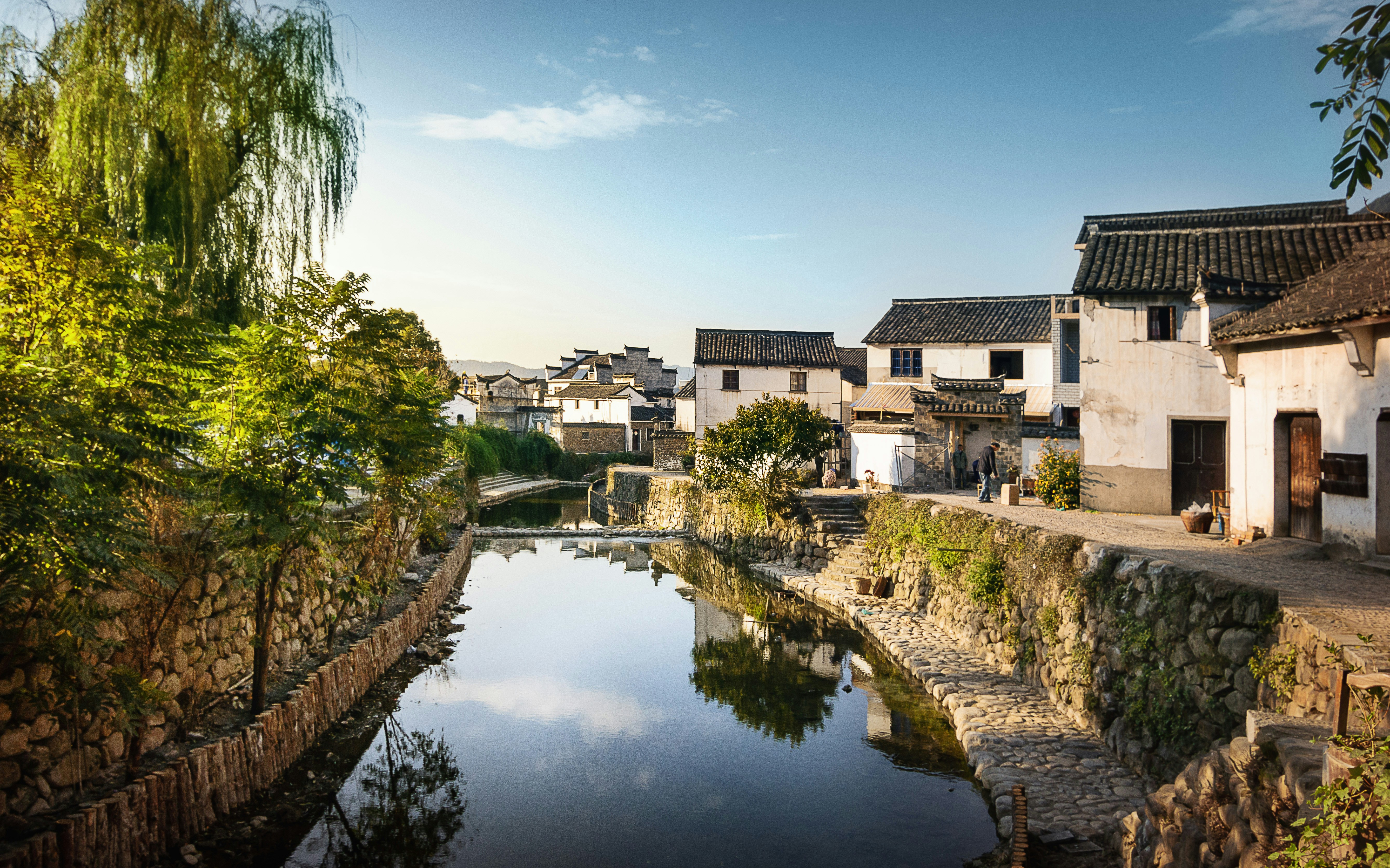 A picturesque riverside scene showcasing traditional architecture along a calm waterway, with lush greenery framing the view.
