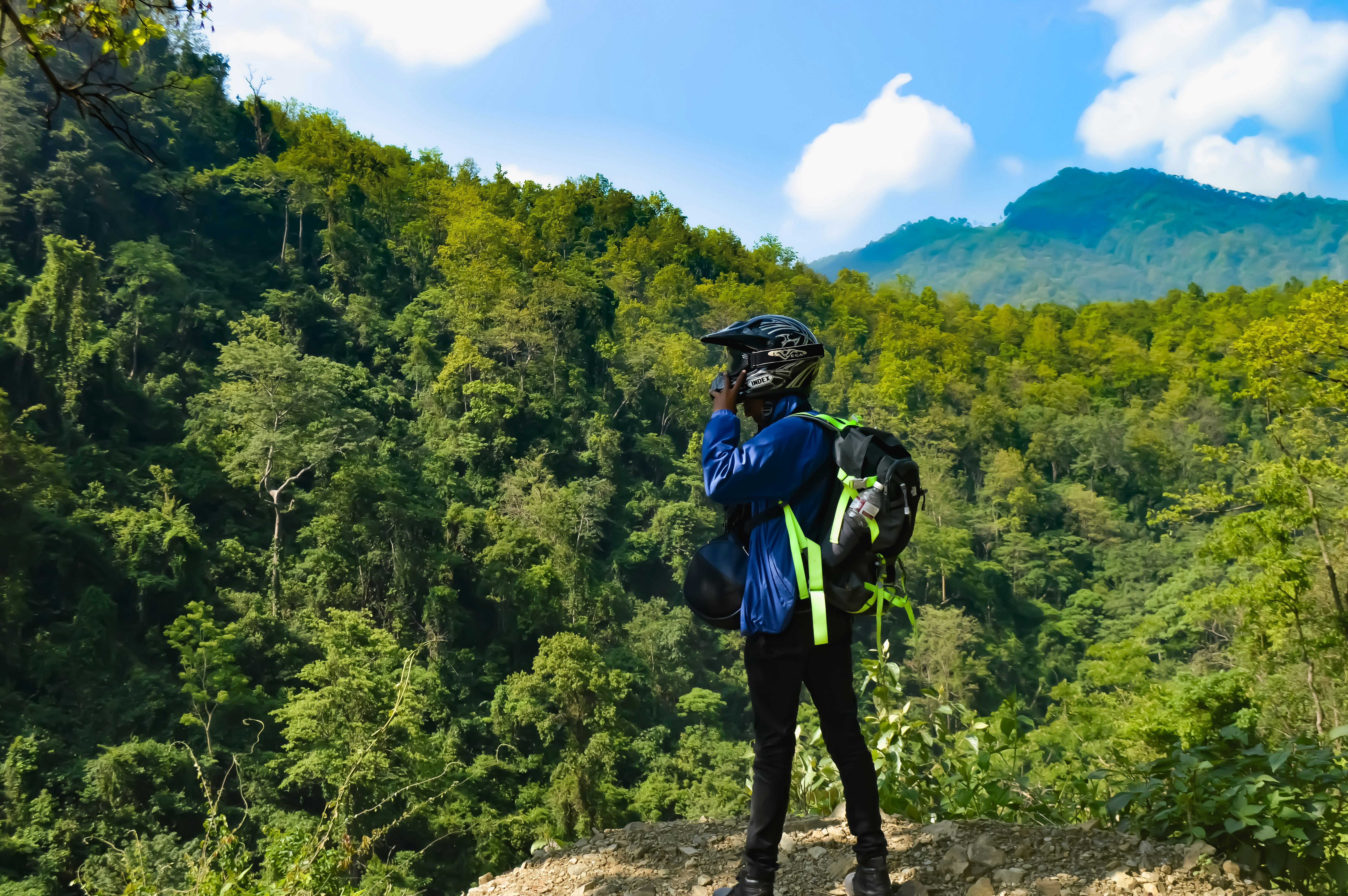 A lone adventurer stands atop a rocky outcrop, gazing at the lush green mountains and sky. The scene captures the spirit of exploration and tranquility.