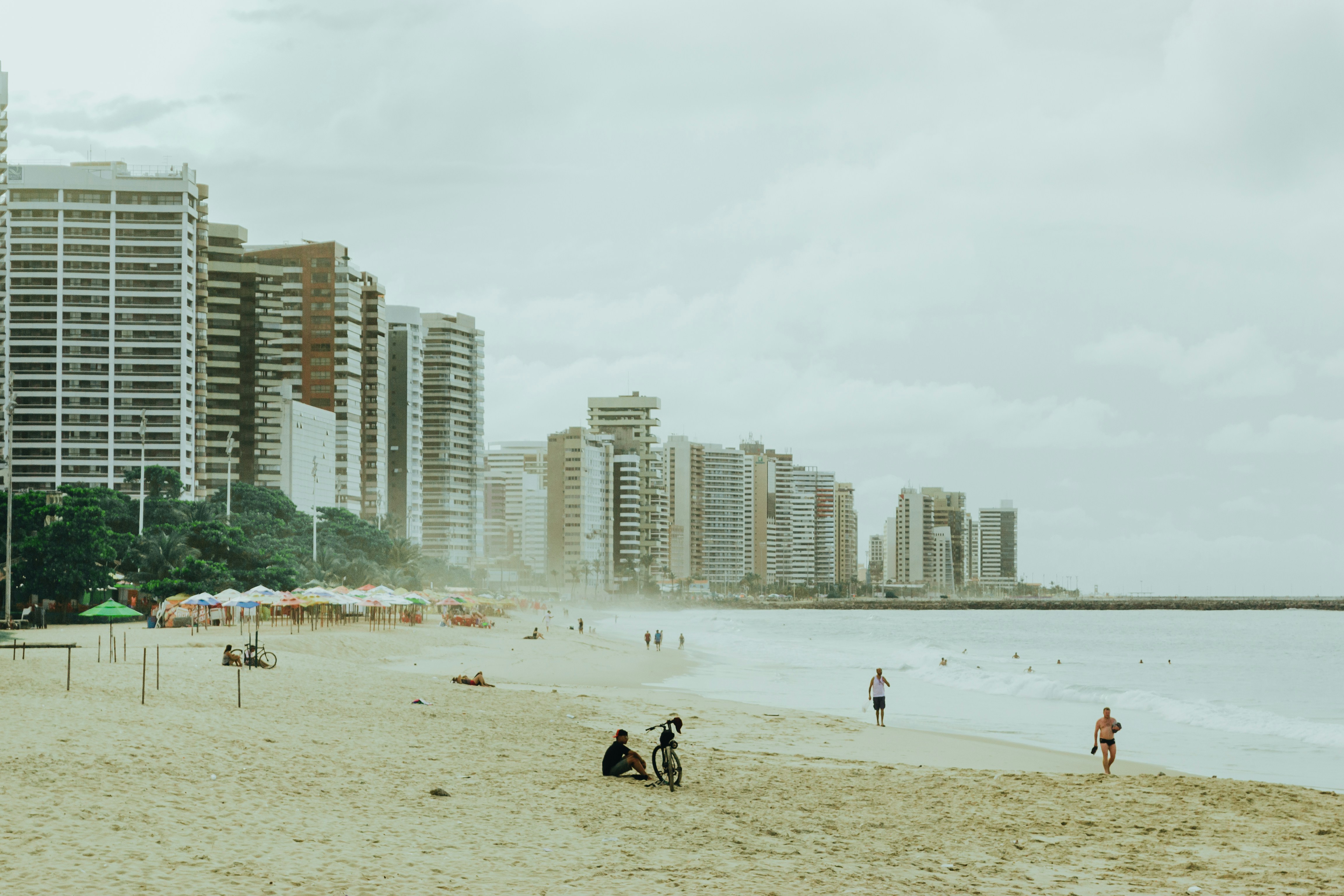 High-rise buildings lining a sandy beach with people enjoying the coastal atmosphere. The scene captures a blend of urban life and nature.
