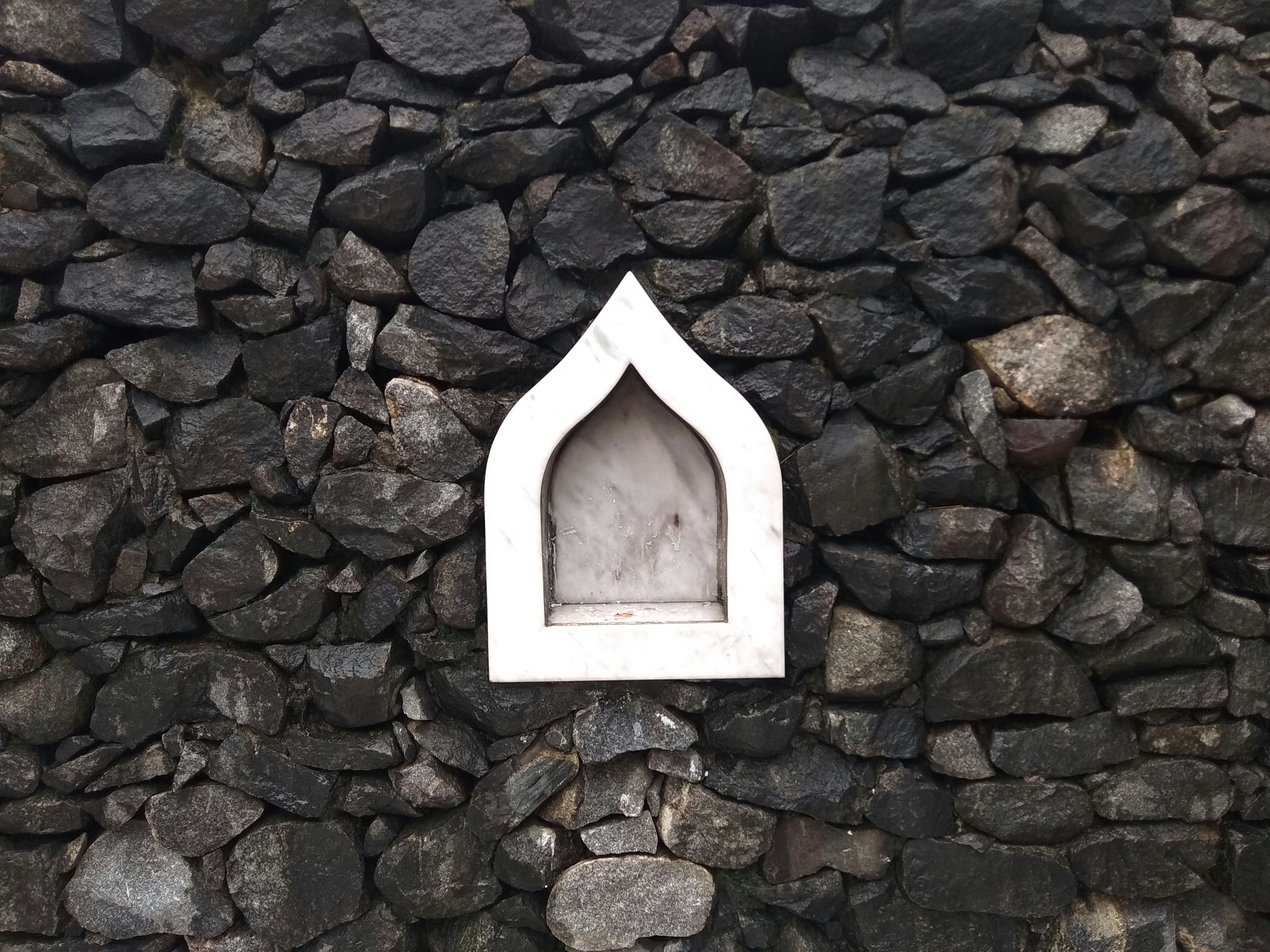 A white arched niche centered on a rough basalt stone wall, forming a stark focal point.