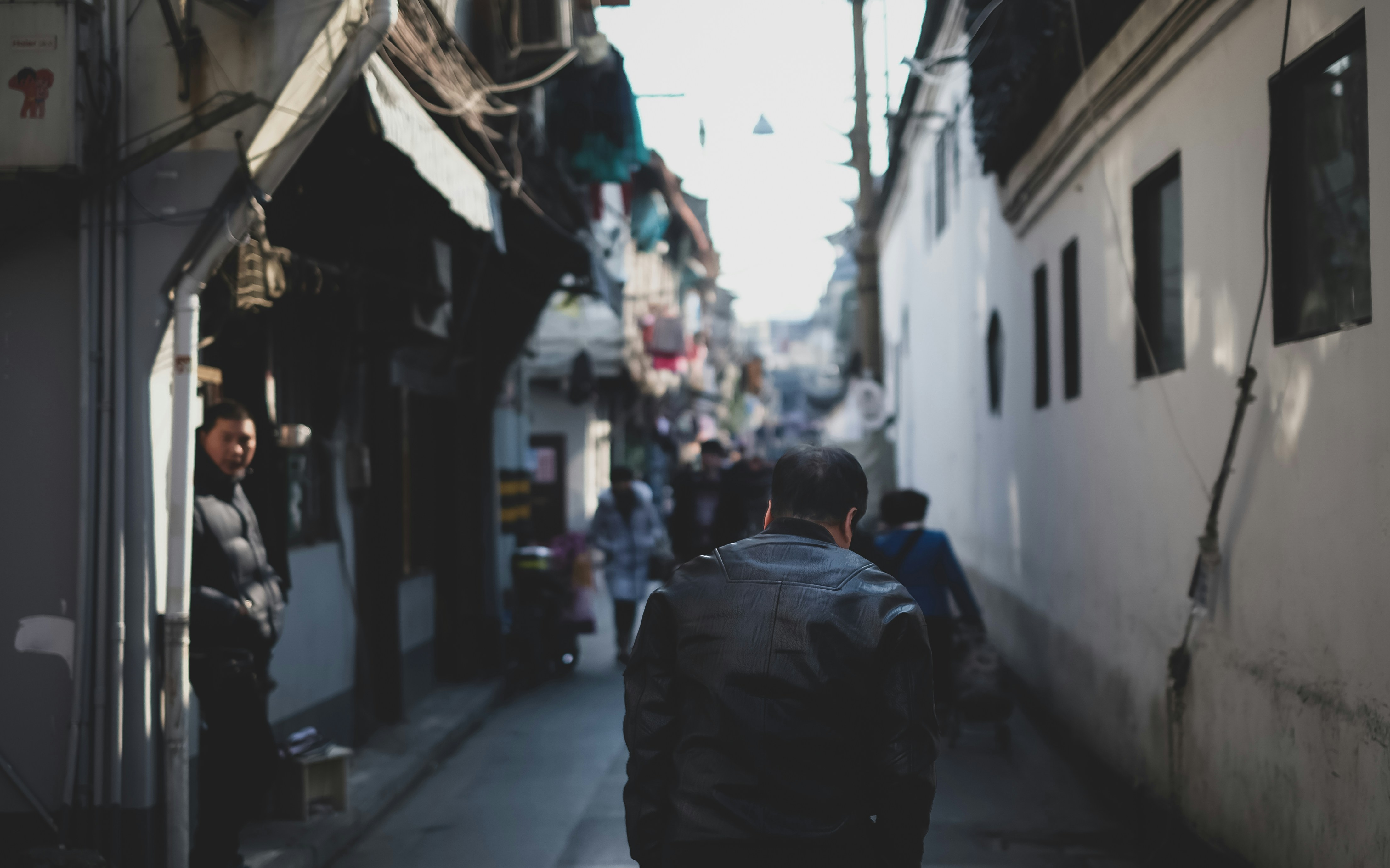 Person walking down a narrow, shadowed alley lined with buildings and hanging laundry.