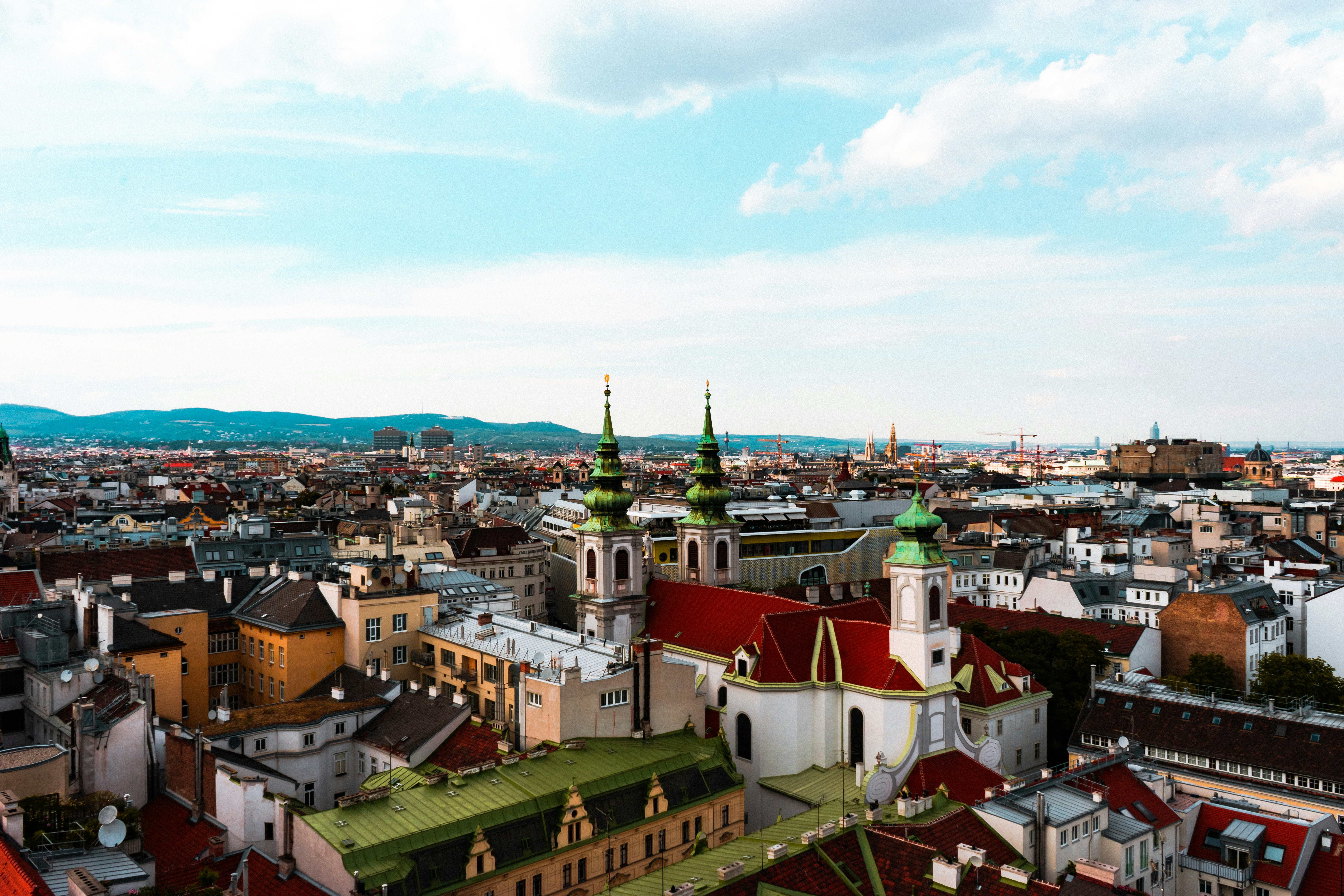 Panoramic view of a cityscape with historic buildings and green spires under a partly cloudy sky.