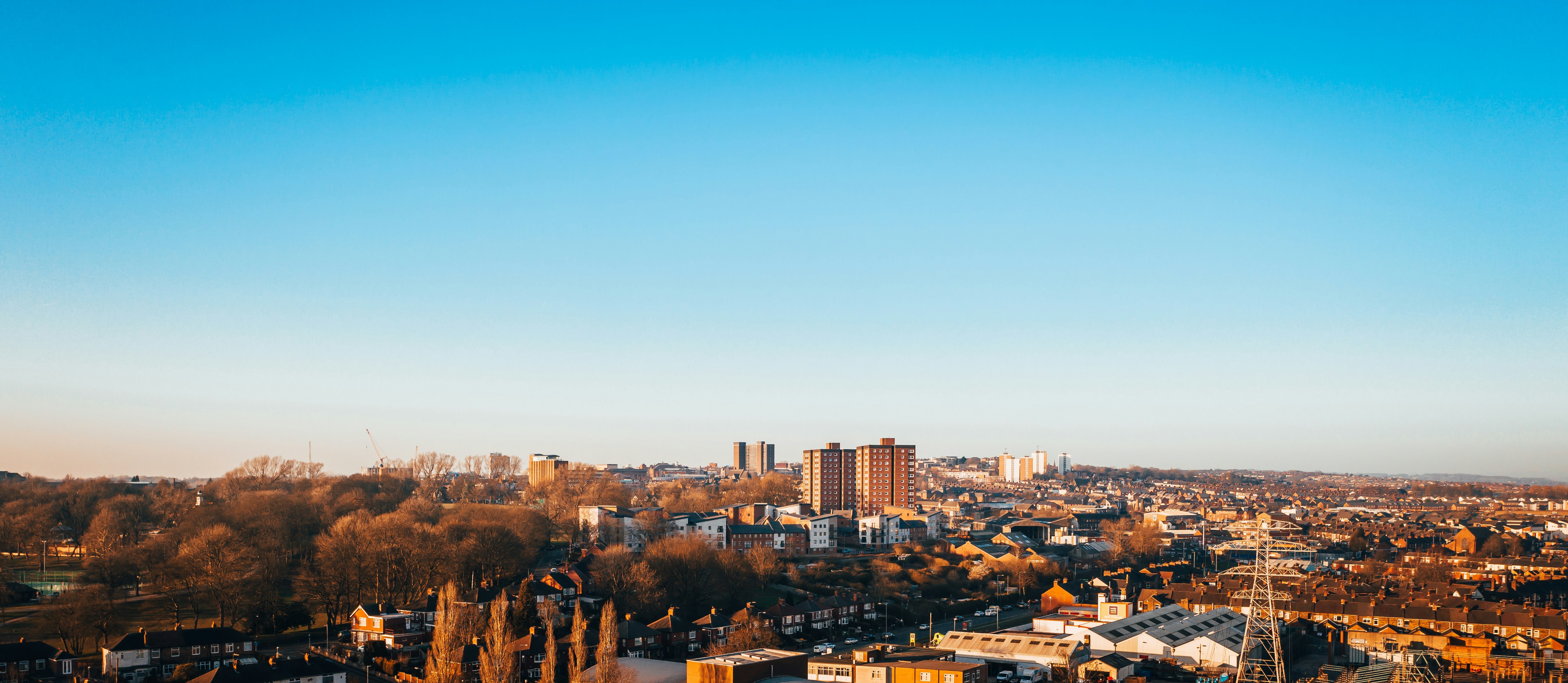 Expansive cityscape under a clear blue sky, captured during golden hour with warm sunlight highlighting the architecture.