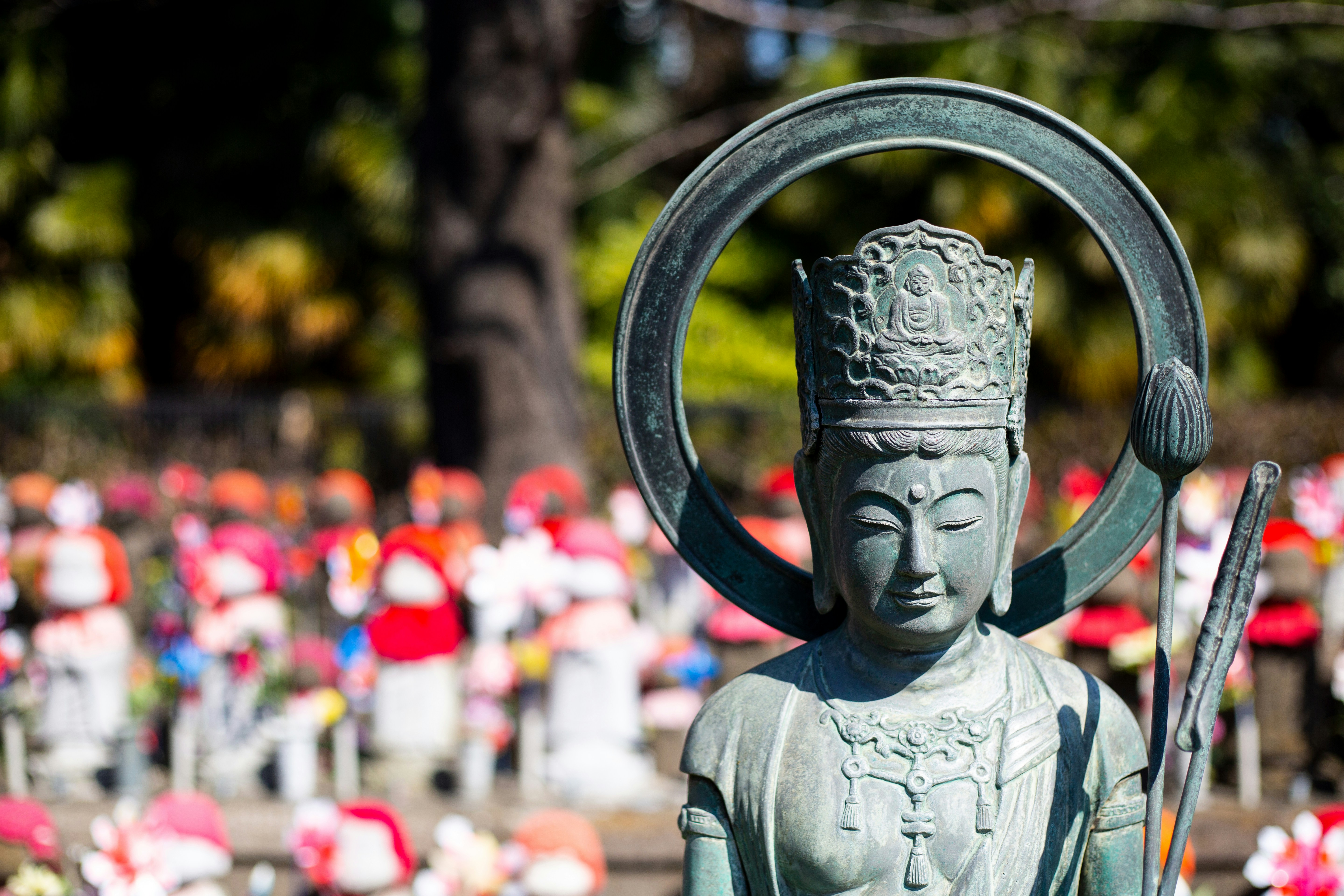 Stone statue of a serene figure at Zojoji Temple, surrounded by colorful child guardian statues.