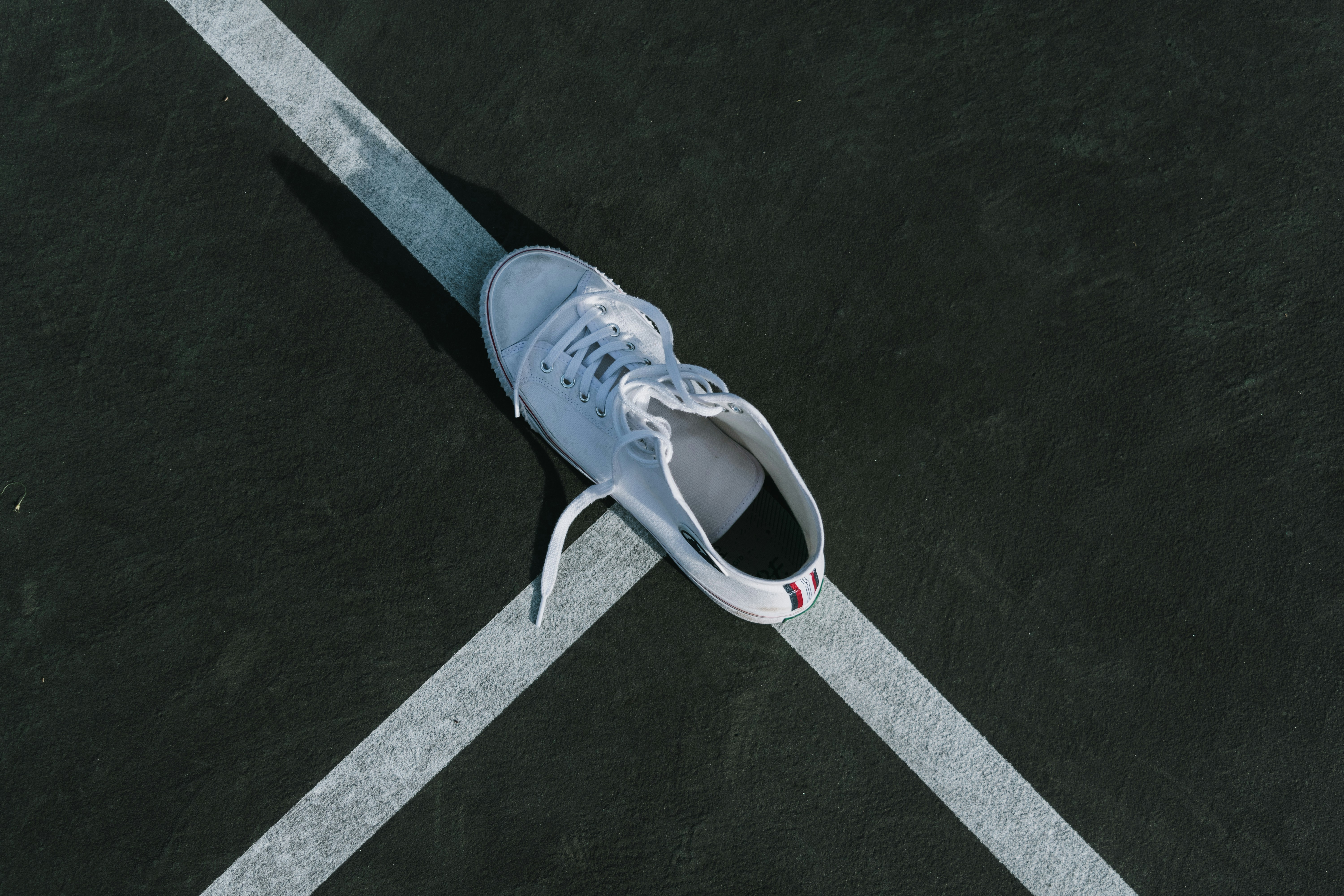 White sneaker resting on a tennis court's marked lines, highlighting the contrast between the shoe and the dark surface.
