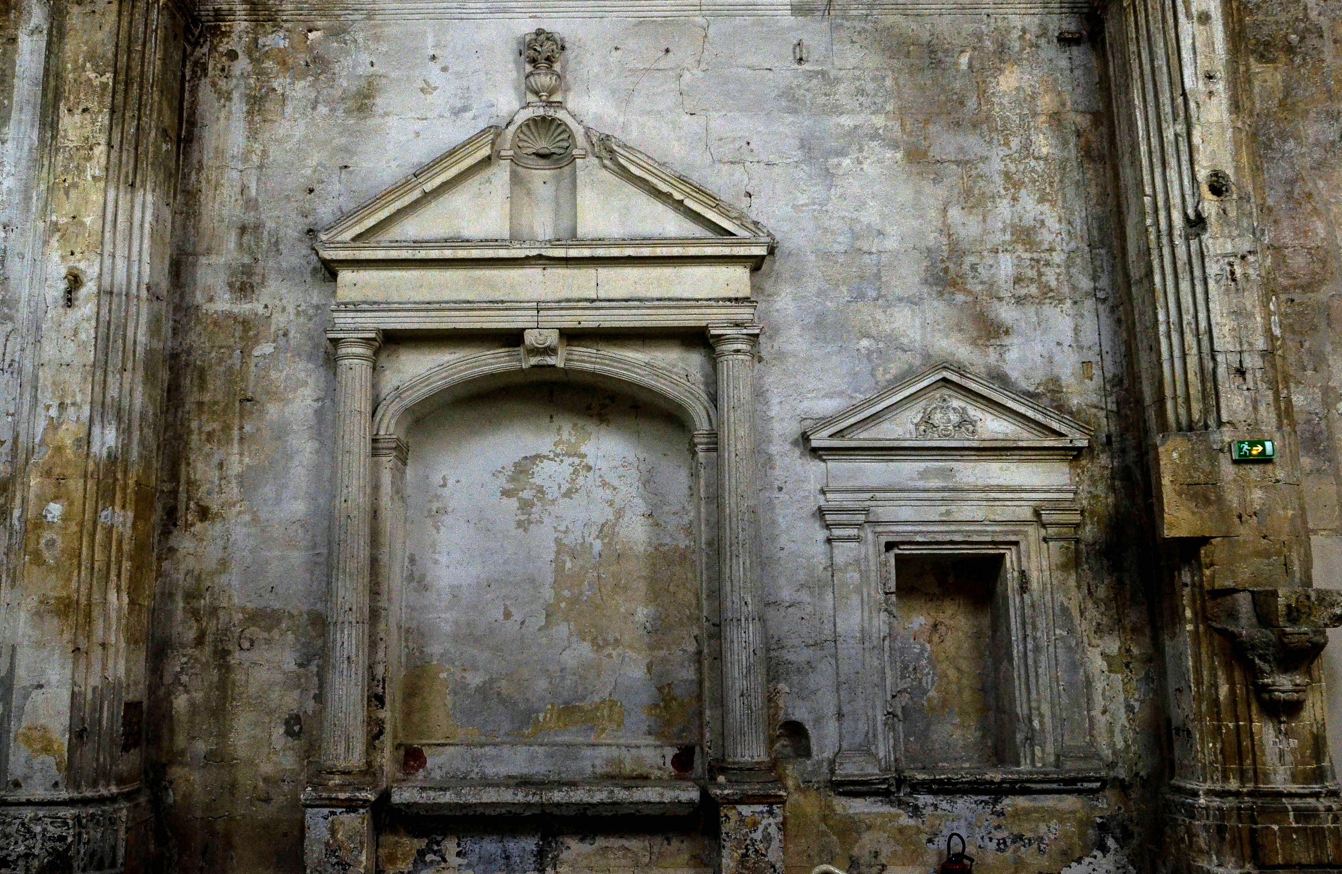 Weathered wall featuring ornate architectural details and empty niches, revealing the passage of time and history.