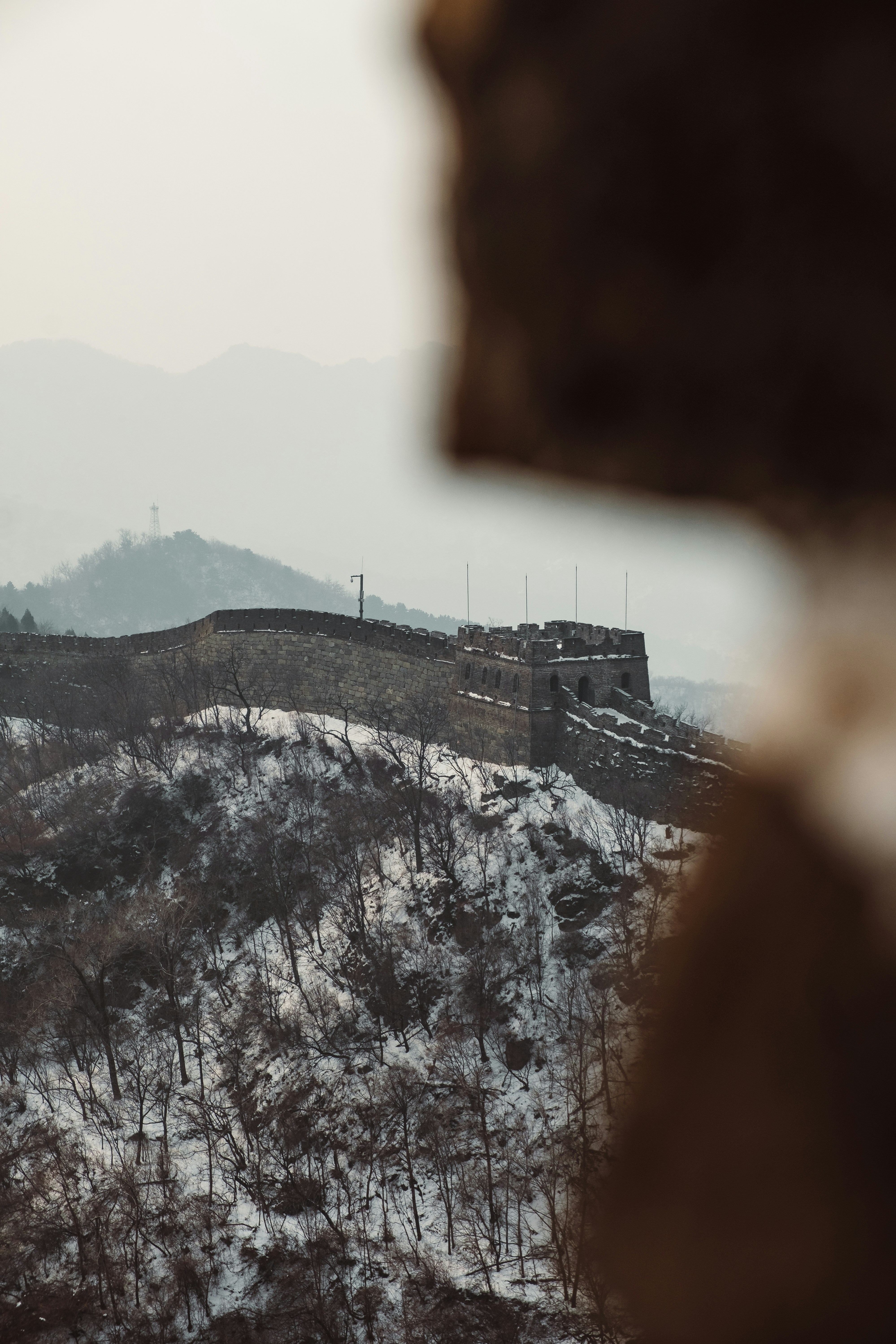 The Great Wall of China stretches across a snow-covered landscape, partially obscured by a rocky foreground. A sense of tranquility envelops the ancient structure.
